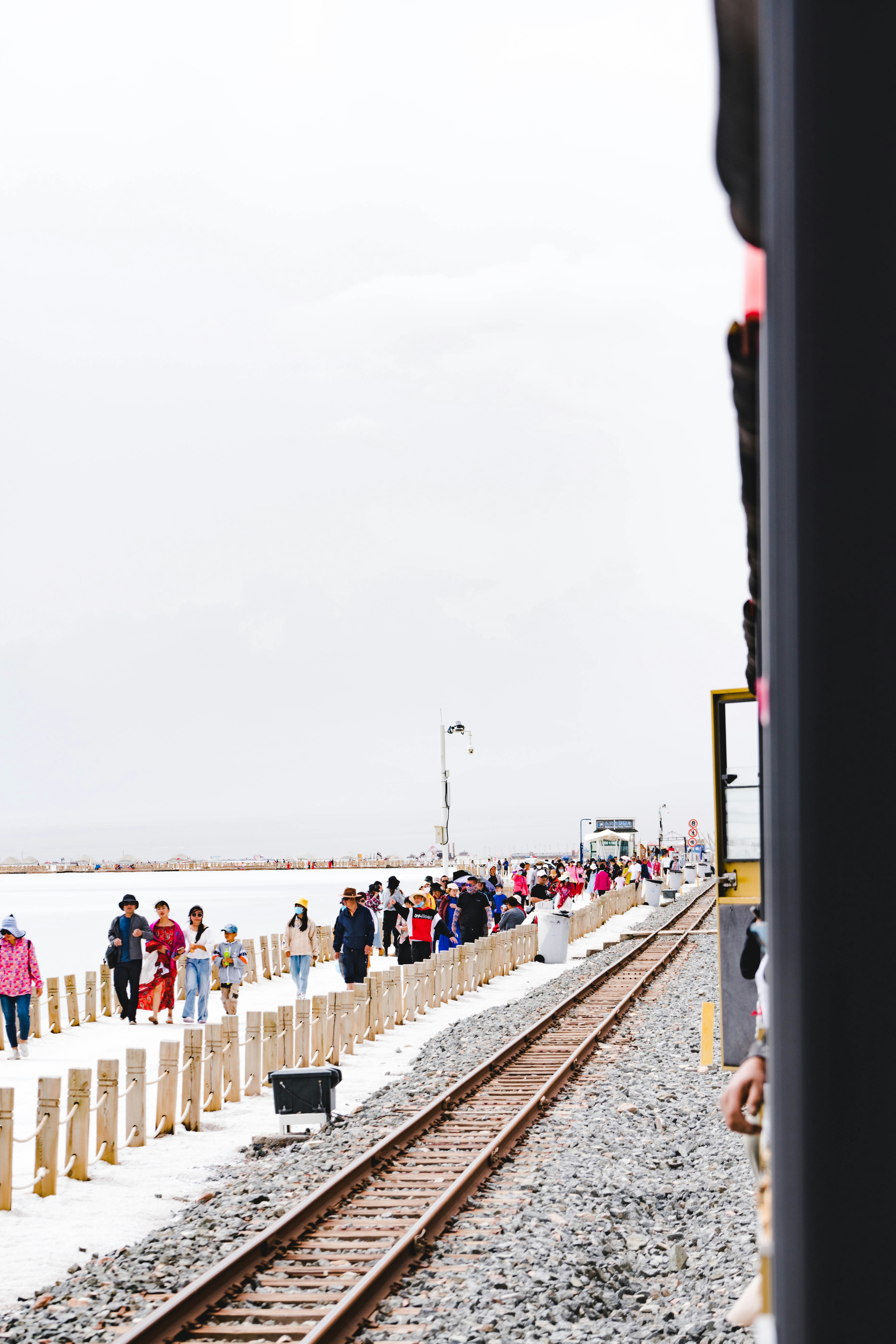 Railing of People by the Distant Shoreline: A Train Track Perspective