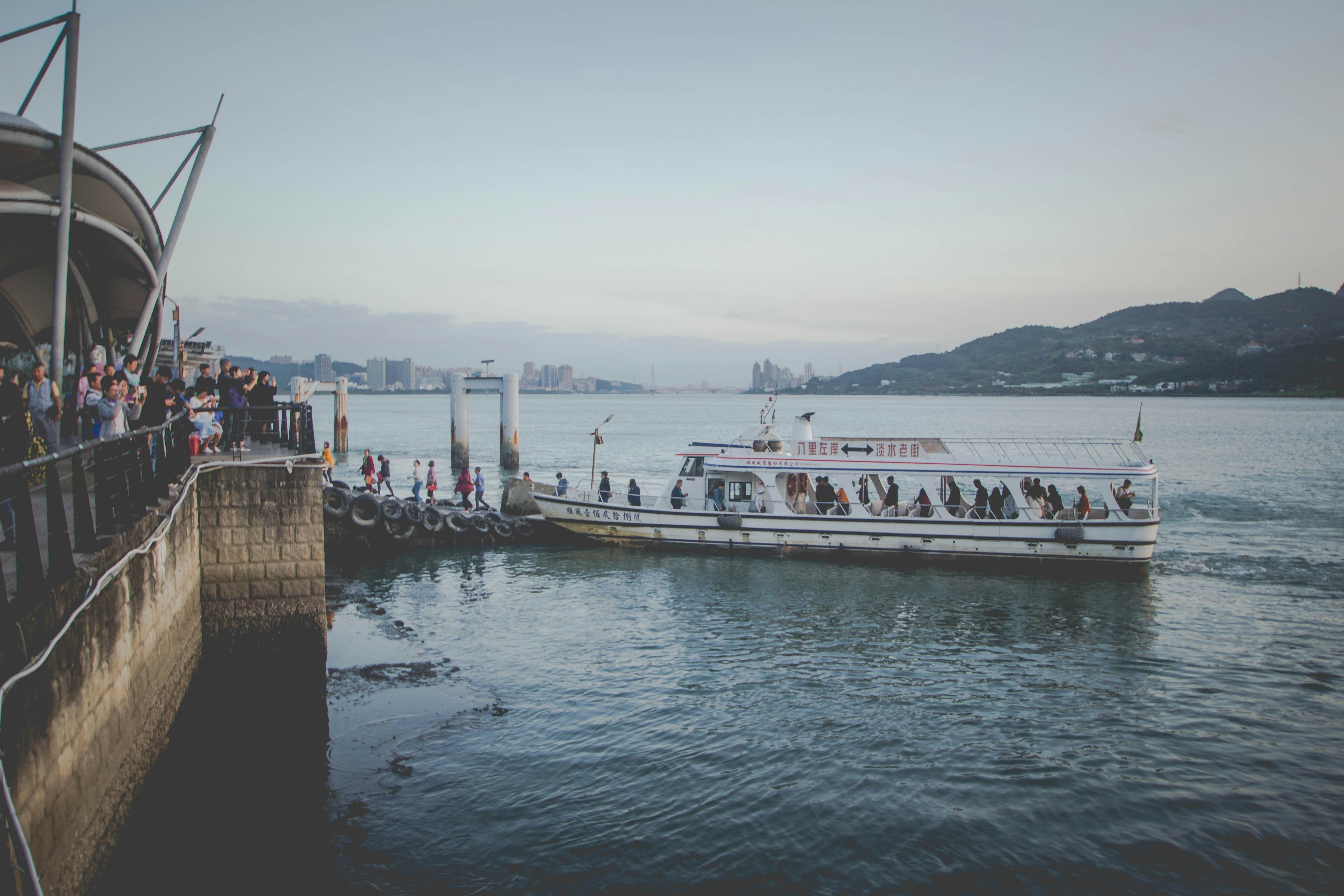 A ferry approaches the dock, filled with passengers ready for adventure, while a crowd gathers along the waterfront. 