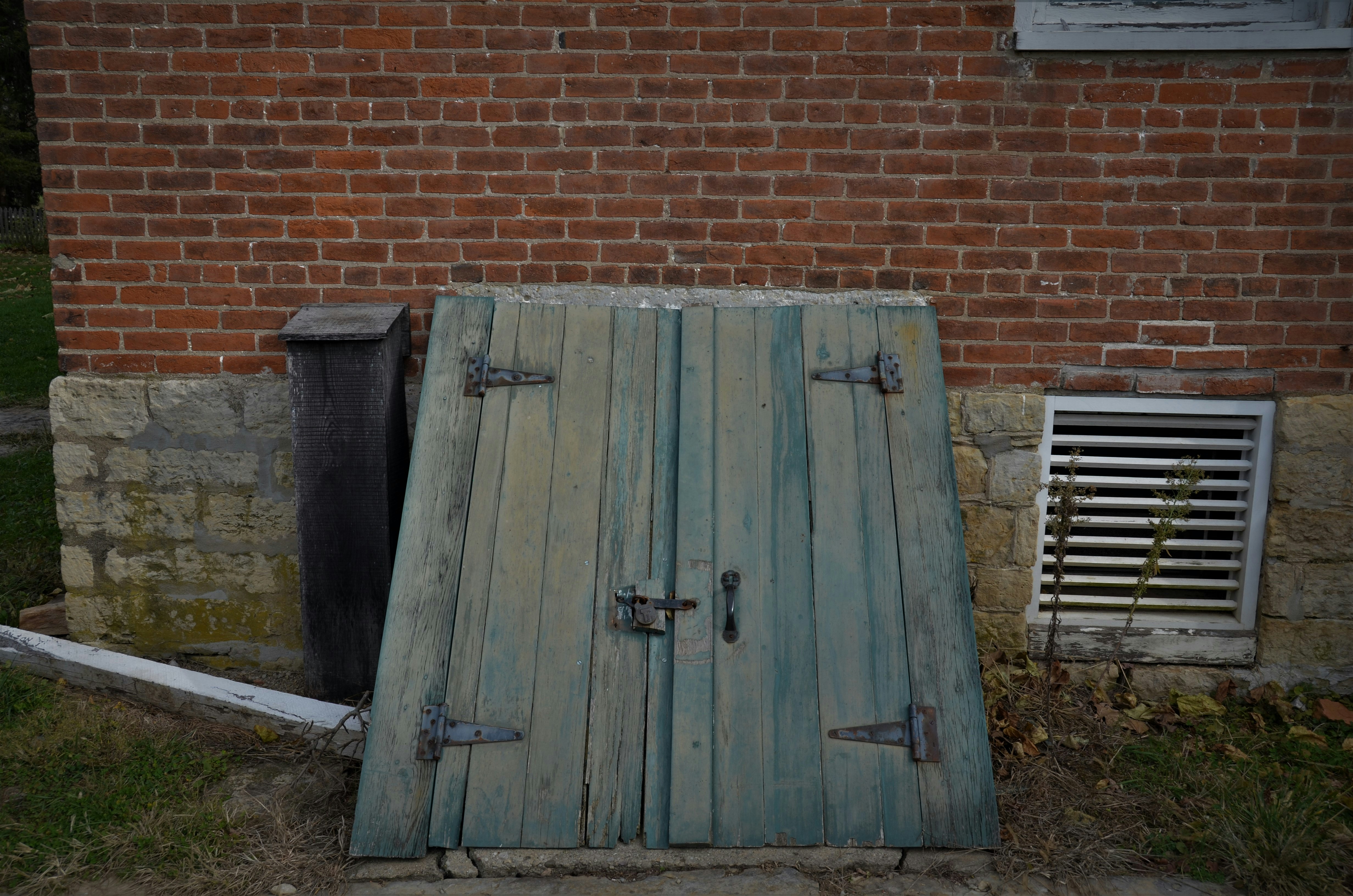 Slanted Blue-Green Hatch Leaning Against a Weathered Brick Backdrop