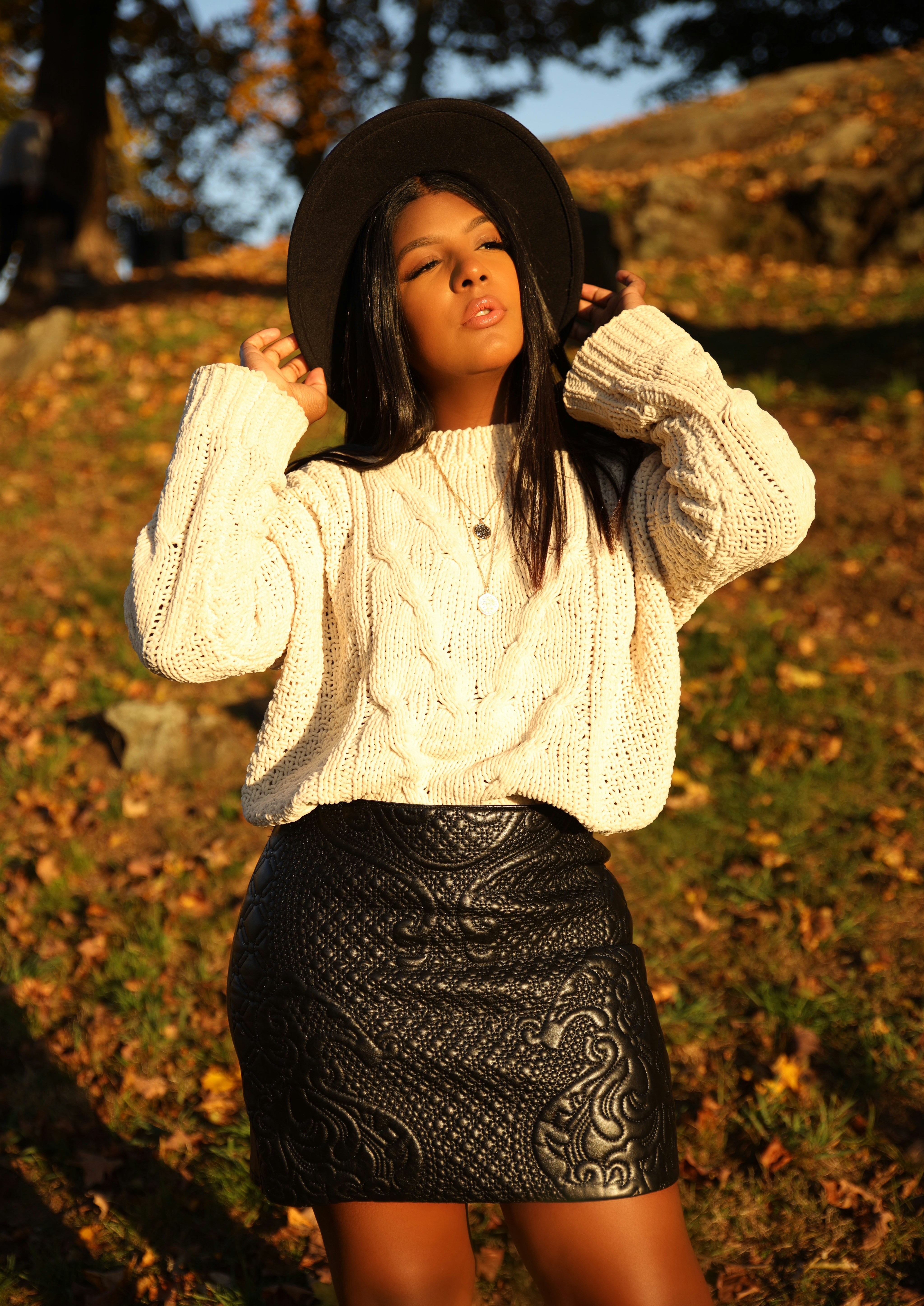 Woman in a cozy sweater and stylish hat poses against a backdrop of autumn foliage, capturing the essence of seasonal fashion.