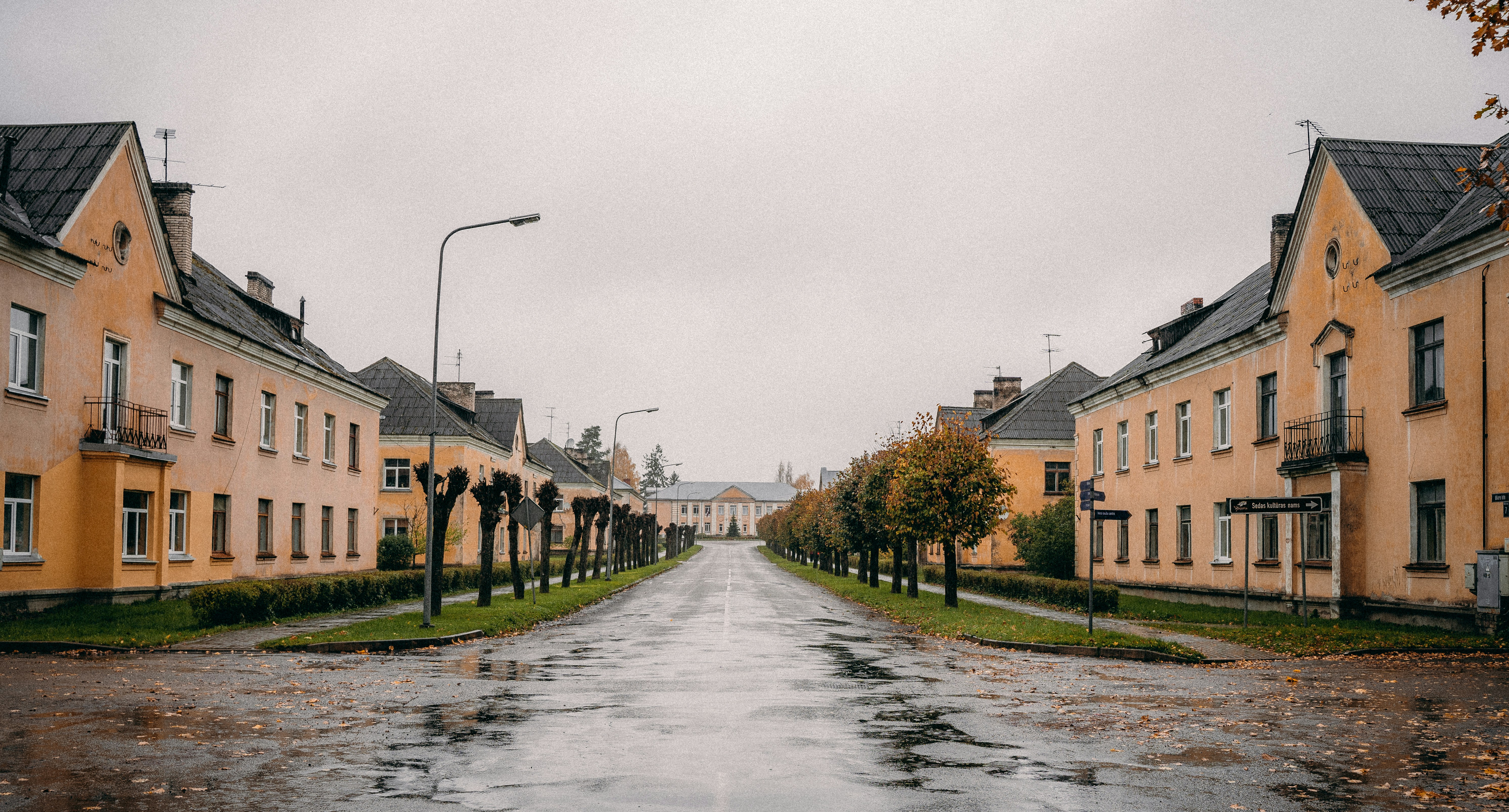 Quiet street lined with pastel-colored buildings and autumn trees, reflecting the stillness of a rainy day.