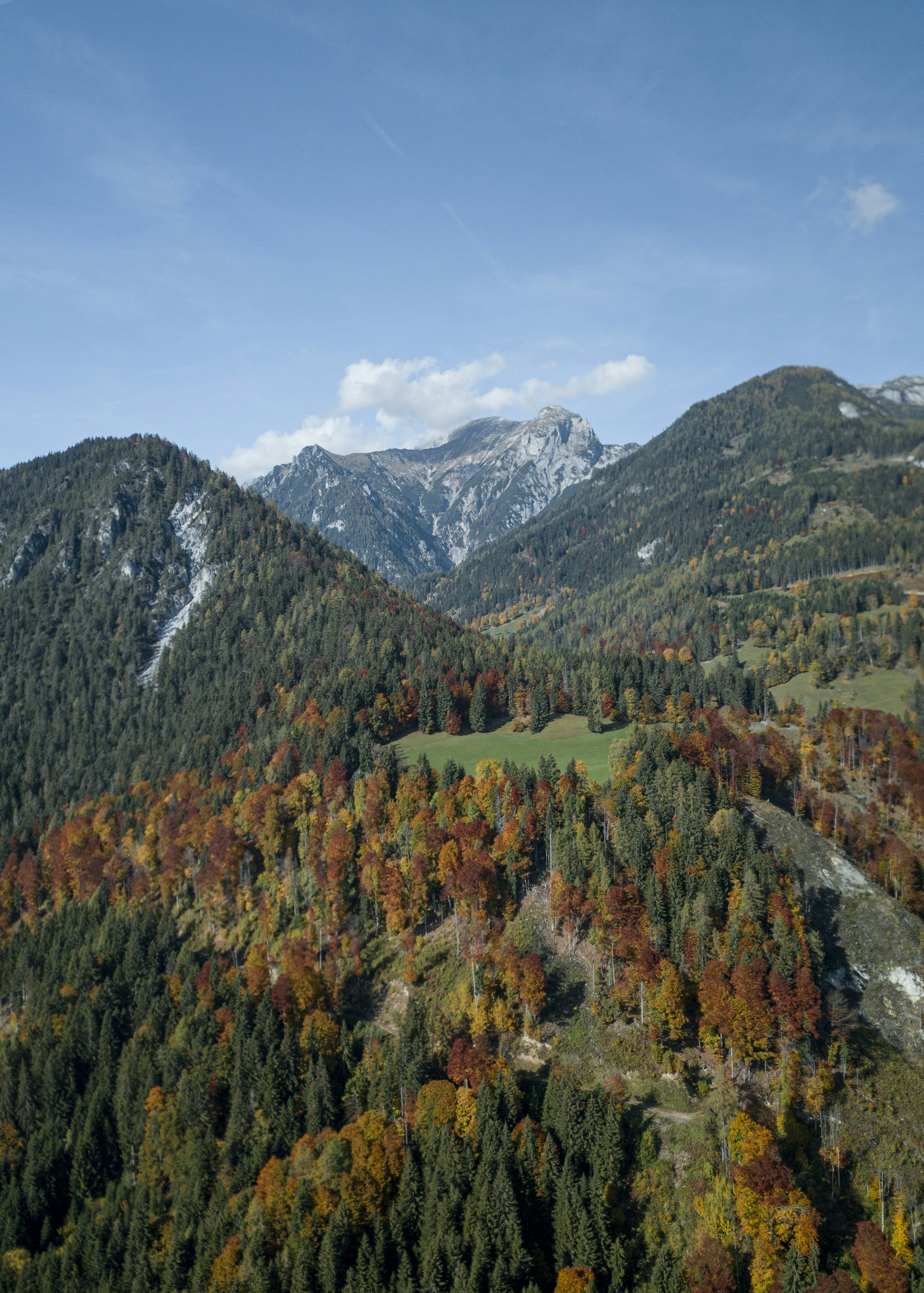 Vibrant autumn foliage blankets the rolling hills, contrasting against the rugged mountain backdrop under a clear sky.