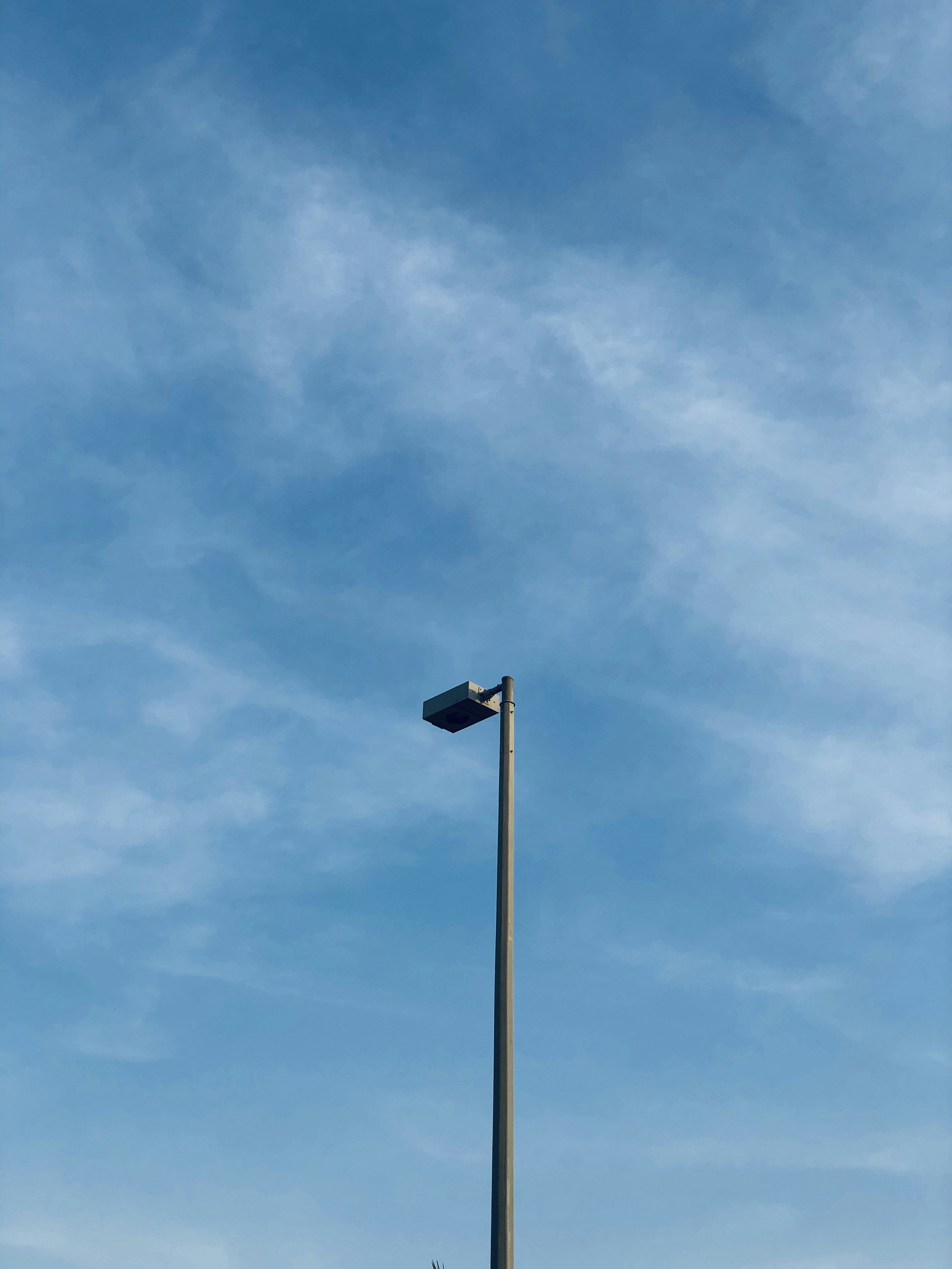 A solitary streetlight towers against a backdrop of soft blue skies with wispy clouds.