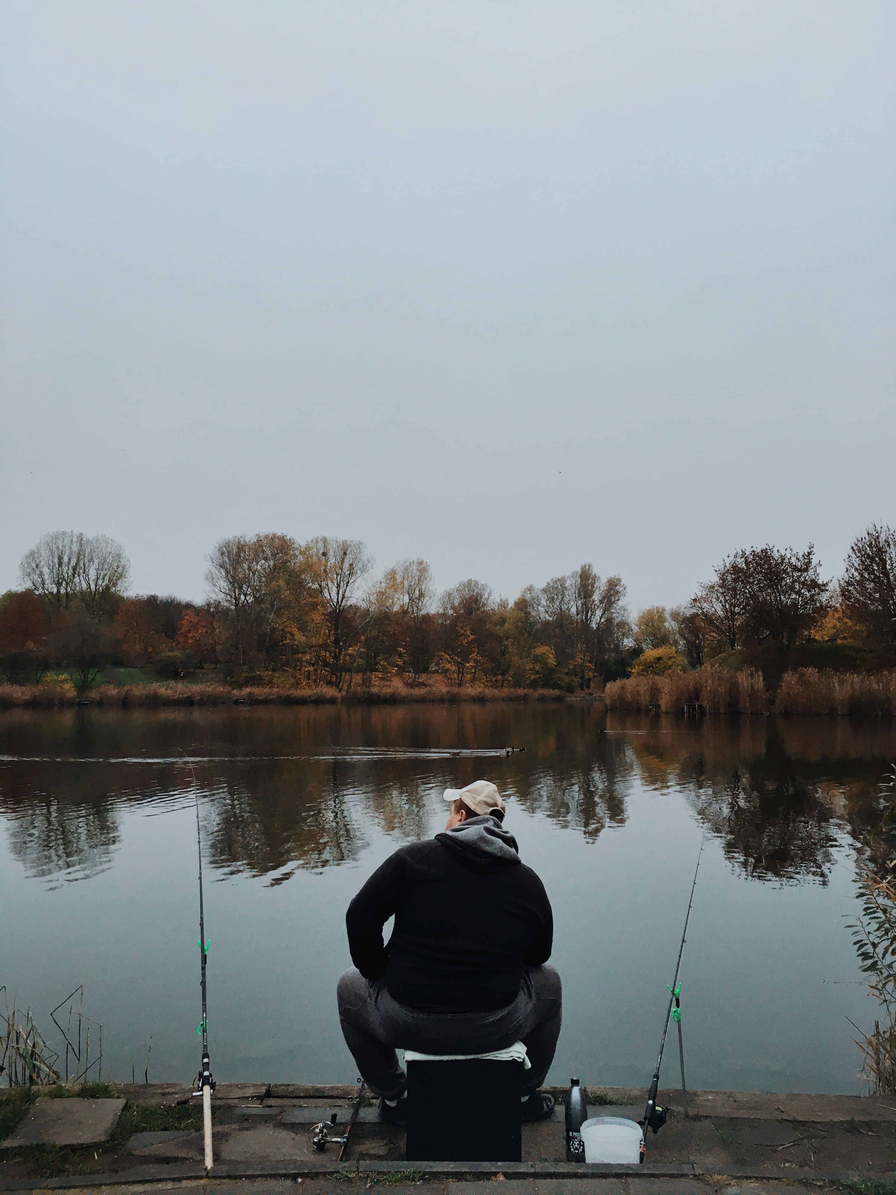 person in black jacket and black pants sitting on rock near lake during daytime