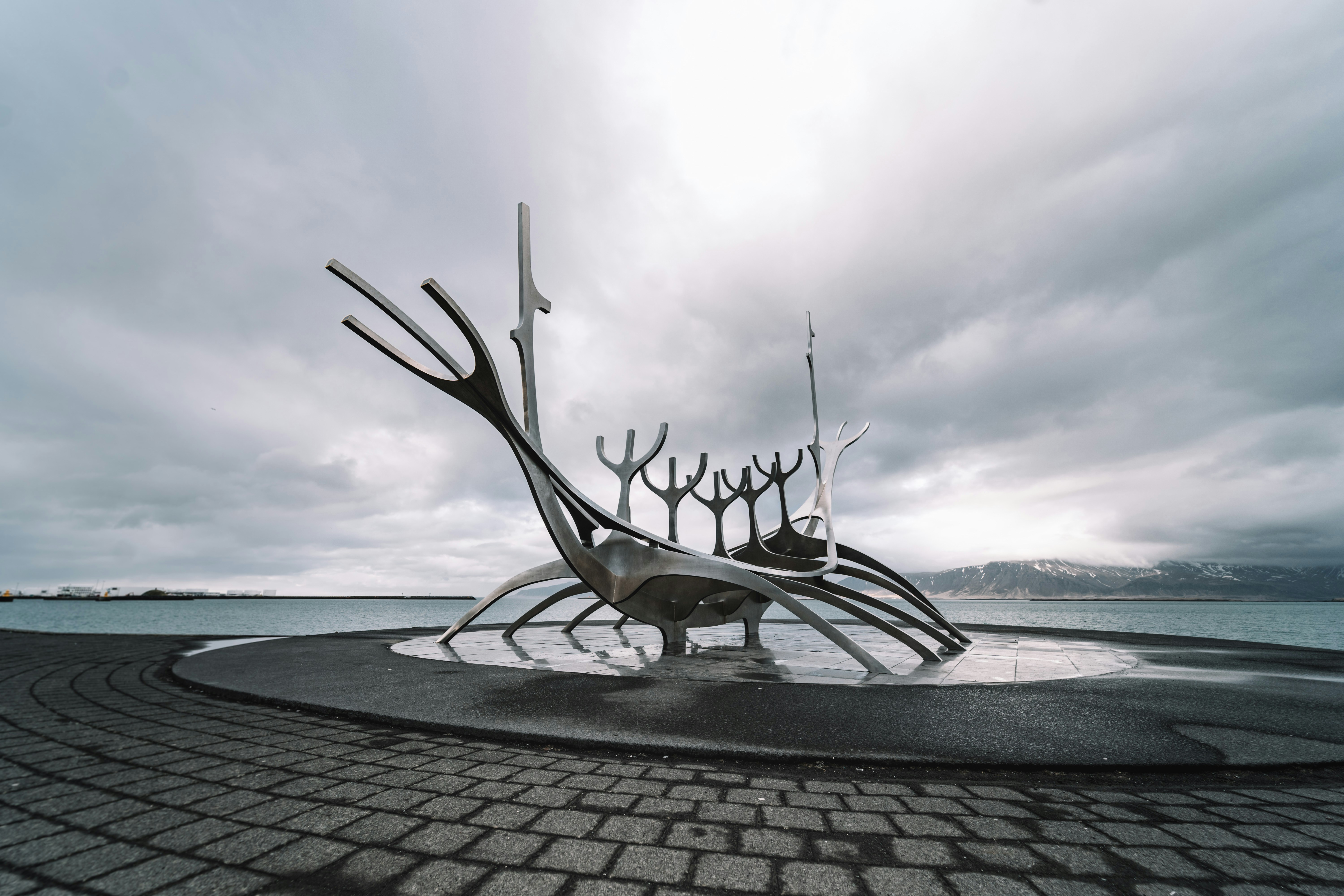 Sculpture of a skeletal ship on a waterfront under a dramatic, cloudy sky.