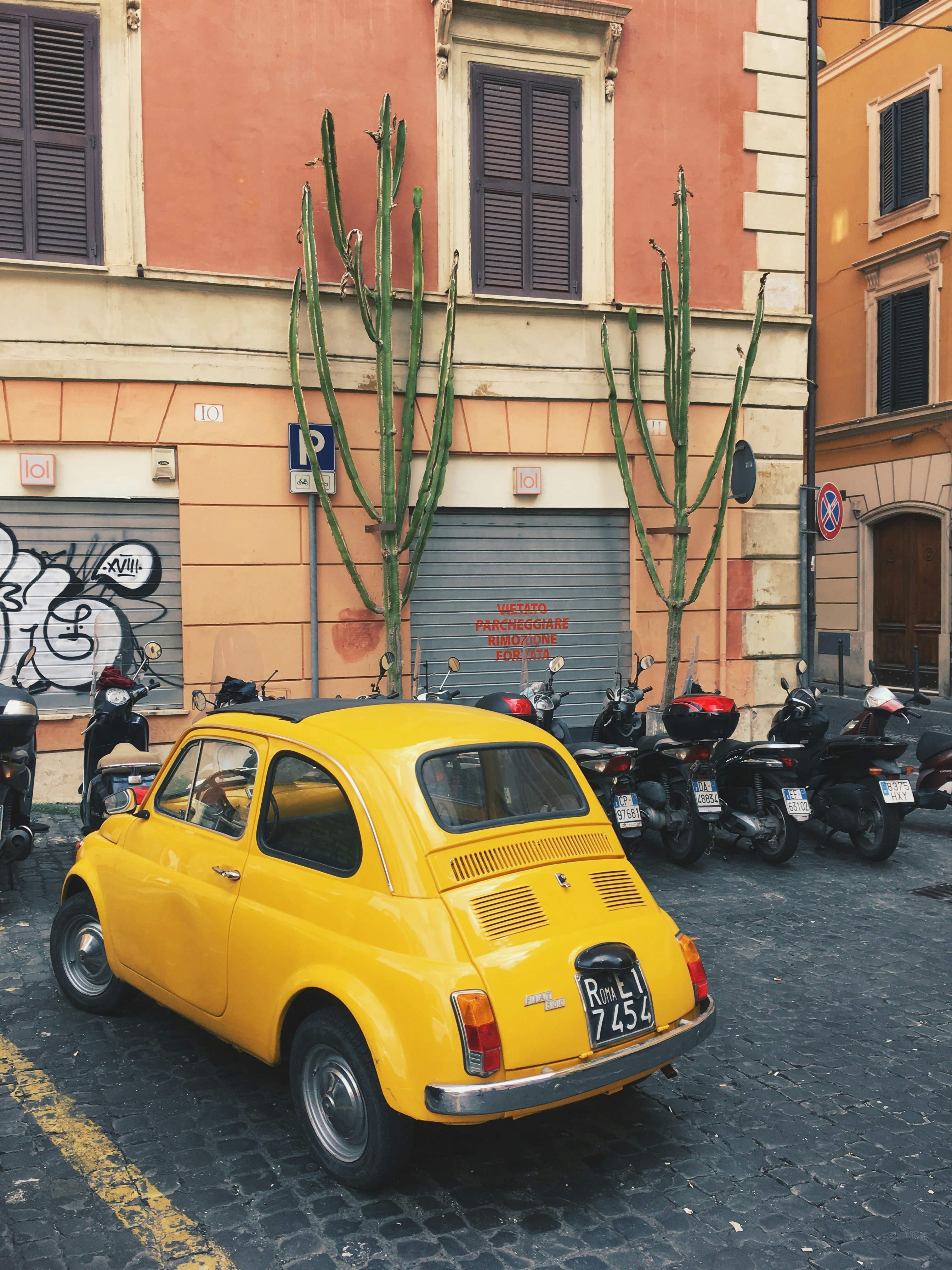 Vibrant yellow vintage car parked near tall cacti against a rustic wall, showcasing a blend of classic and contemporary elements.