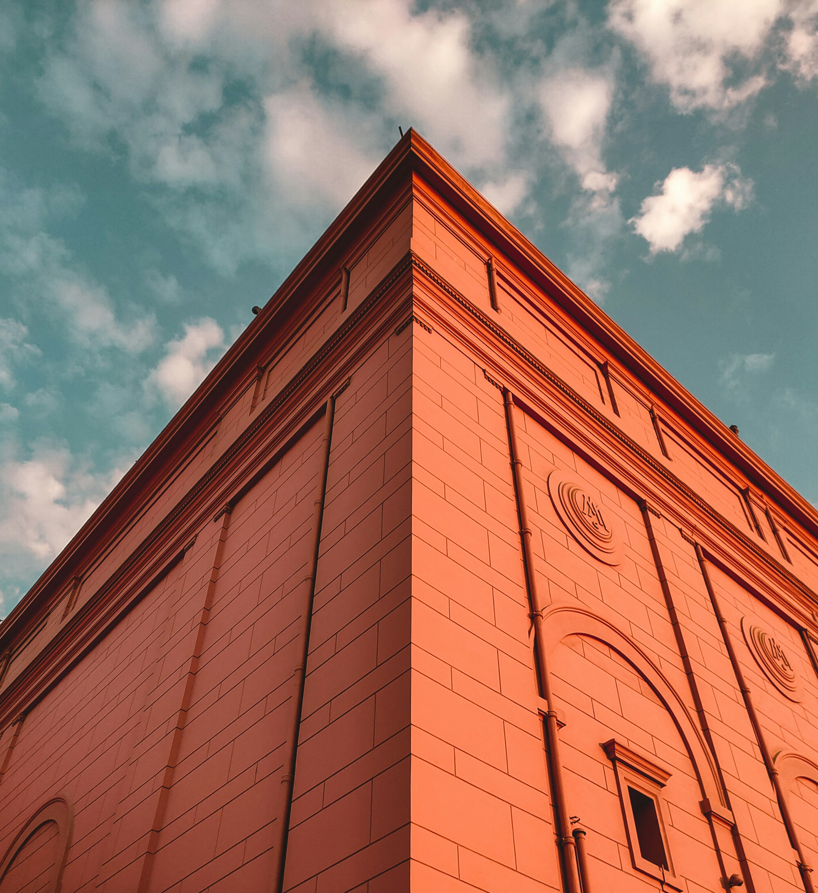 Corner of a tall, ornate building with a warm tone facade set against a partly cloudy sky.