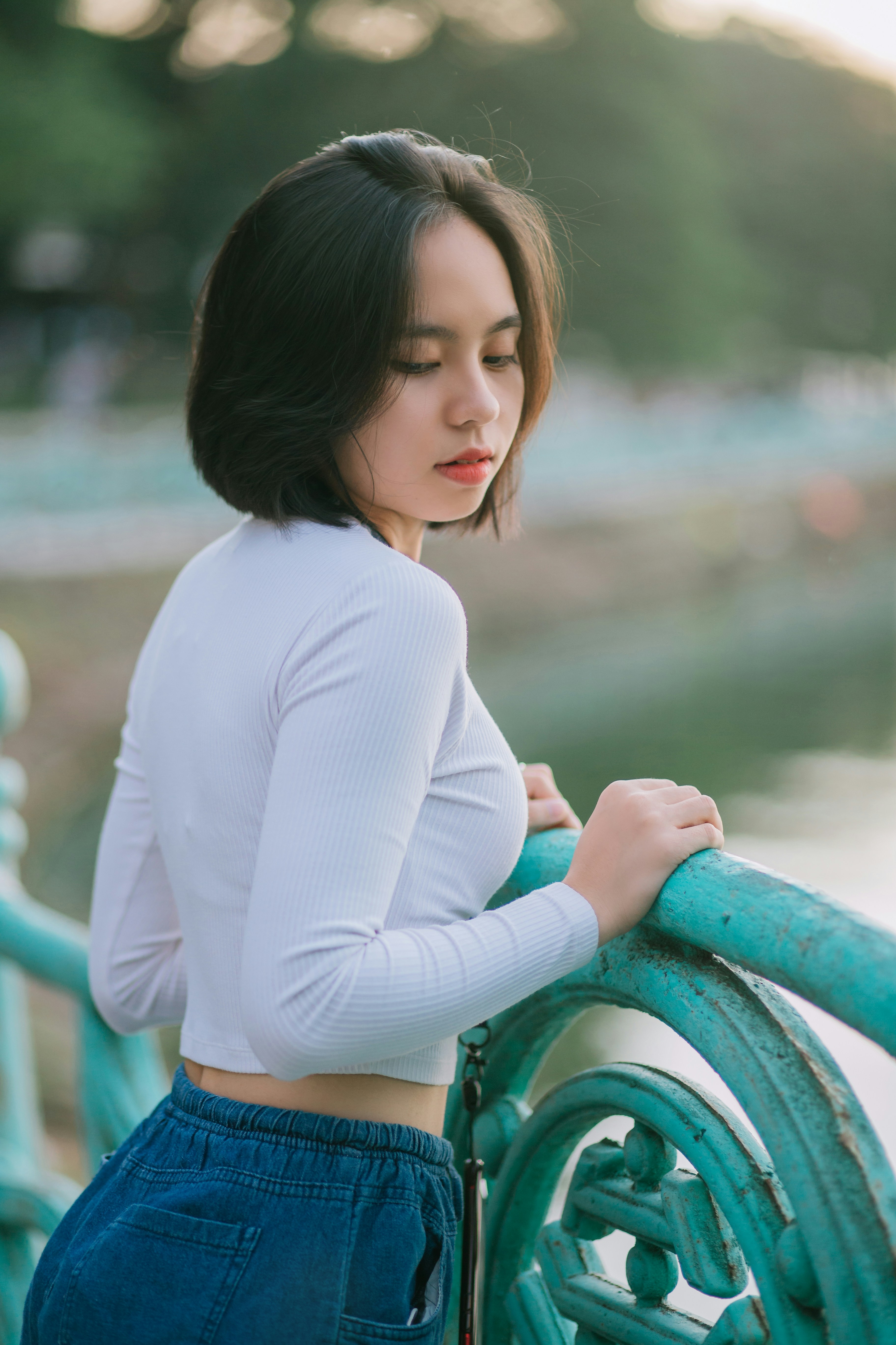 Young woman leaning against a teal railing, lost in thought as she gazes at the water. The soft light enhances the serene atmosphere.