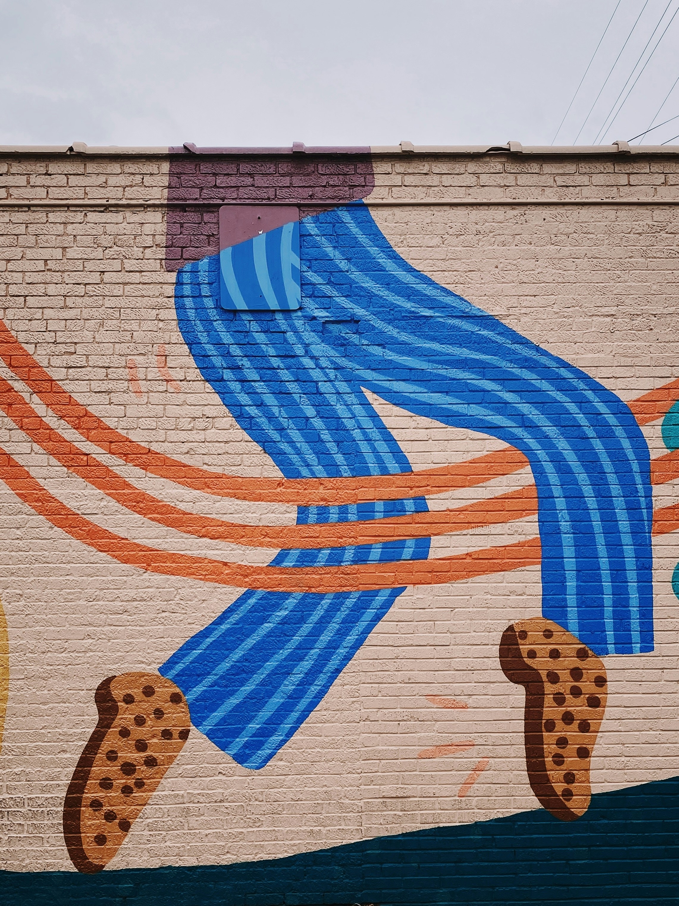 Vibrant mural legs in motion: blue ribbon curves across a brick wall