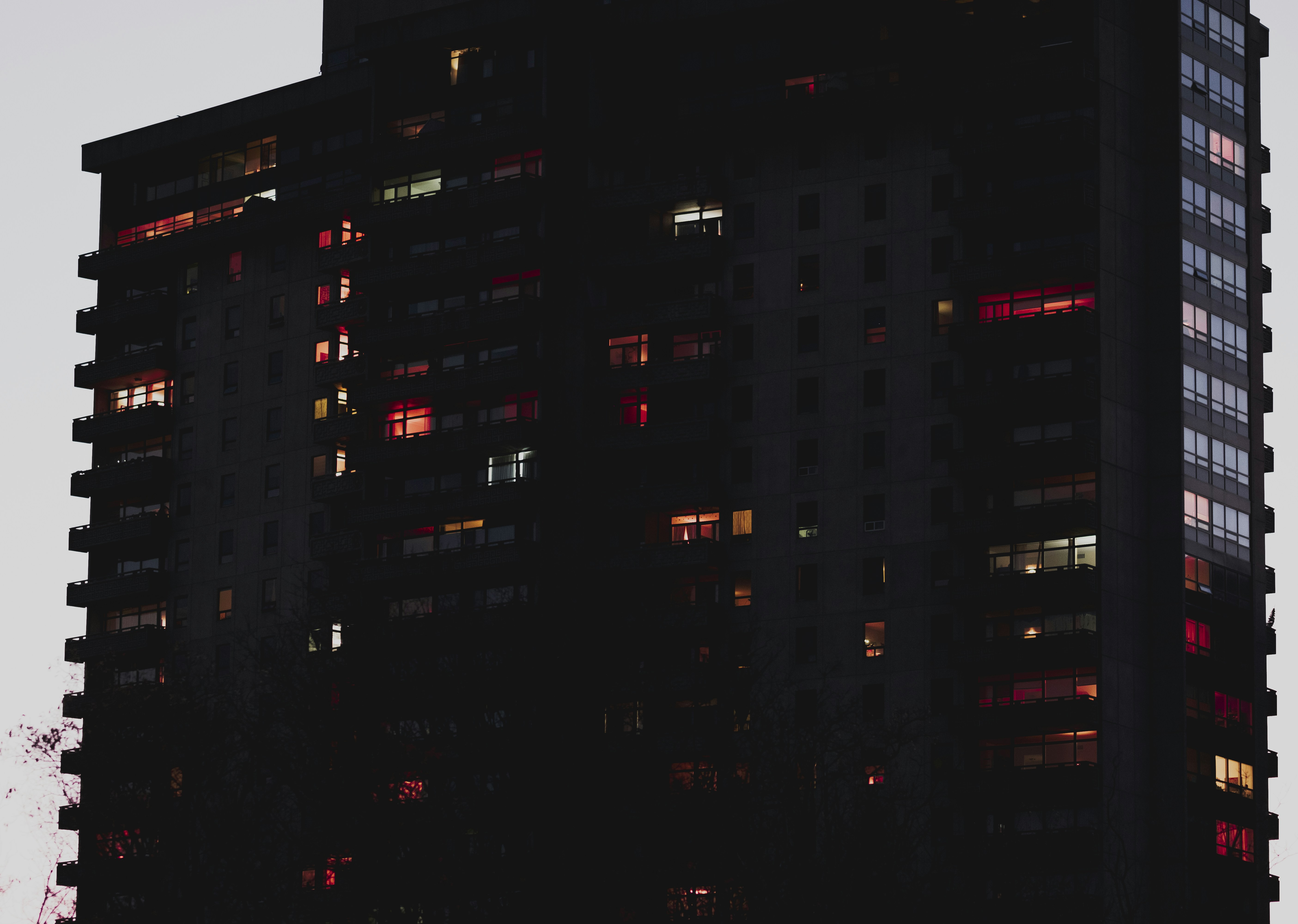 A high-rise building at dusk, its windows illuminated in warm hues, revealing glimpses of life within. The silhouette contrasts against the darkening sky.