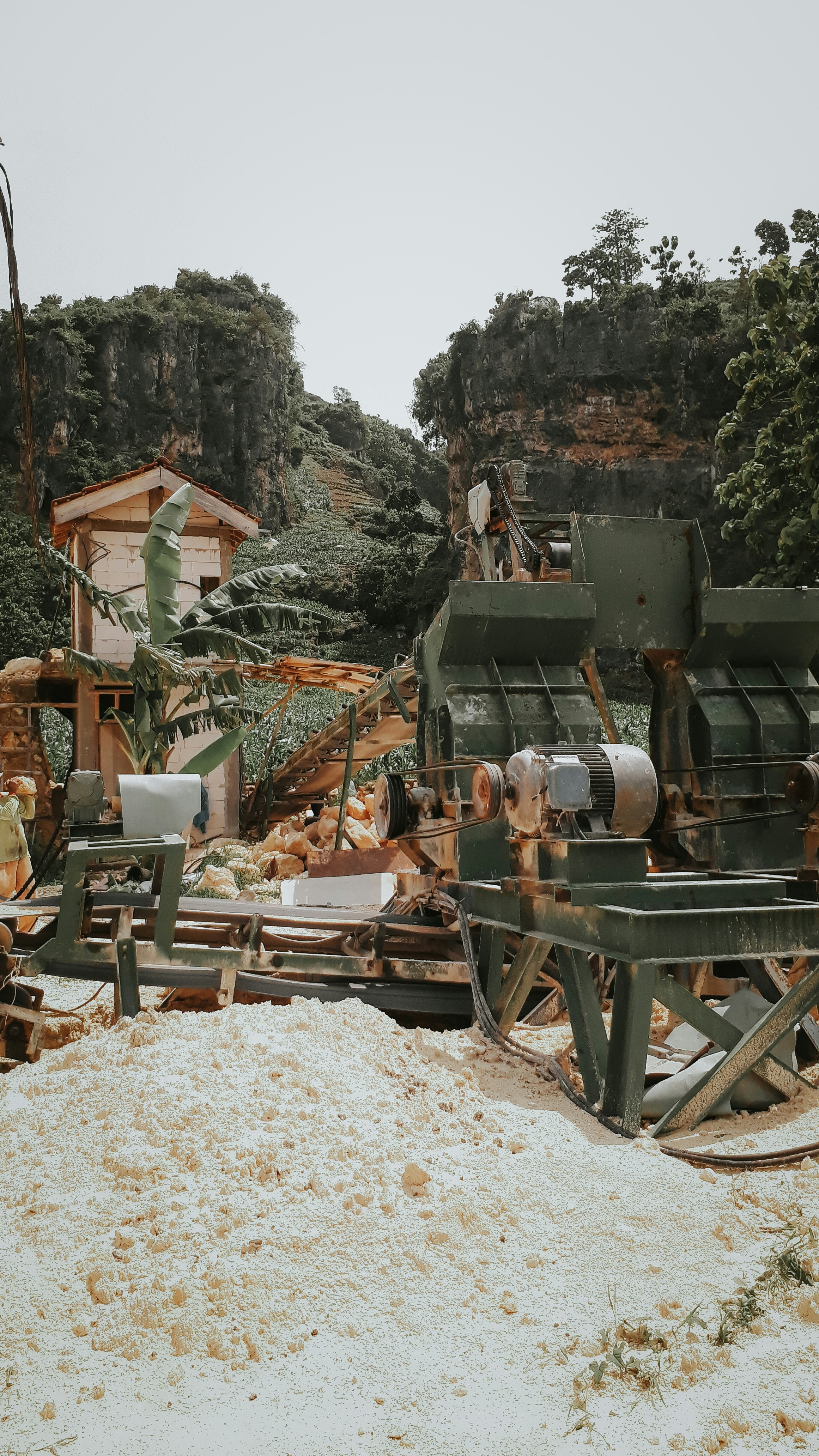 Industrial machinery surrounded by lush greenery and rocky terrain, highlighting the contrast between technology and nature. Dust and debris scatter across the foreground.