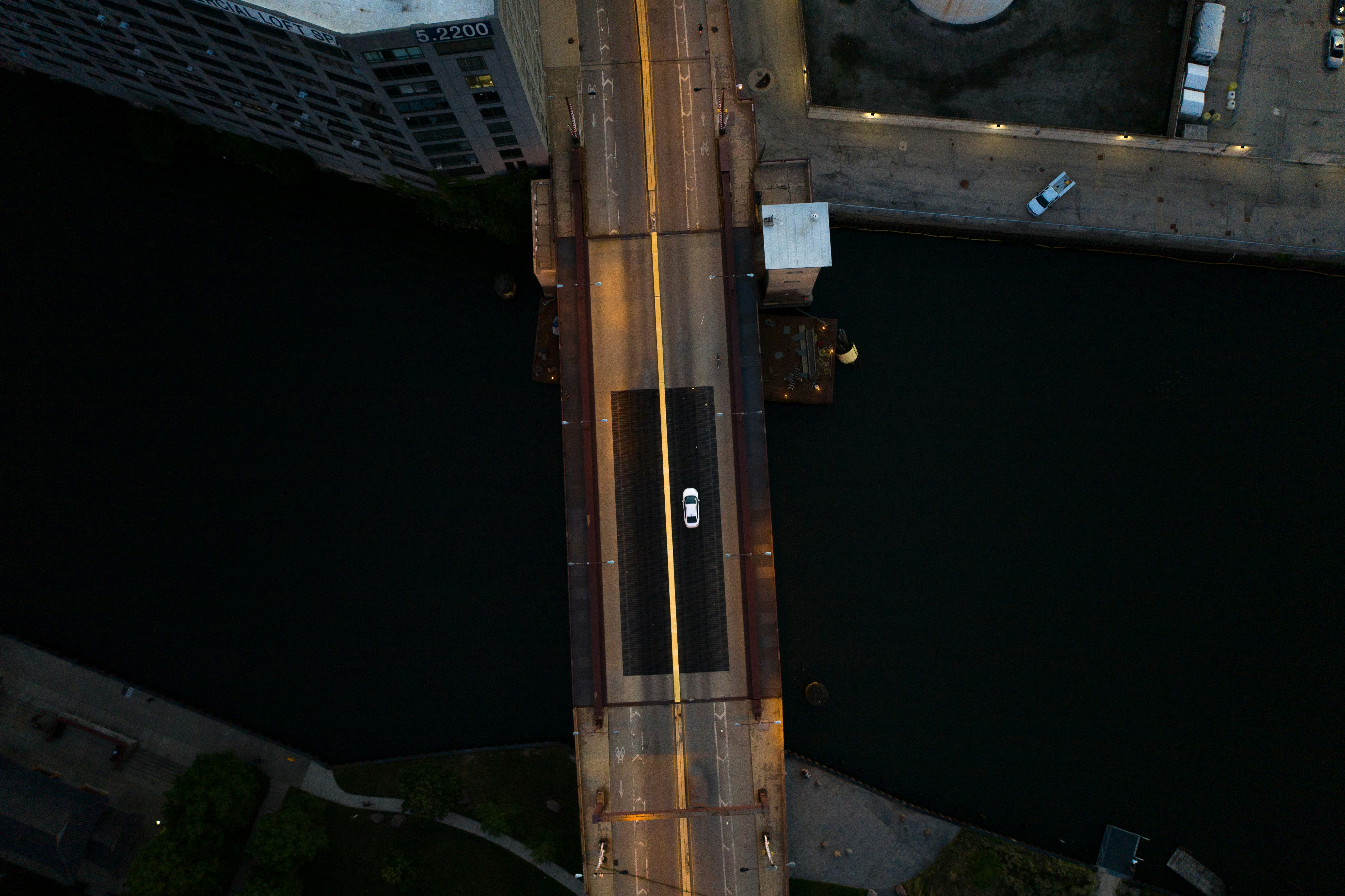 Dusk Bridge Crossing: A lone car traverses a rust-streaked span over a shadowy river