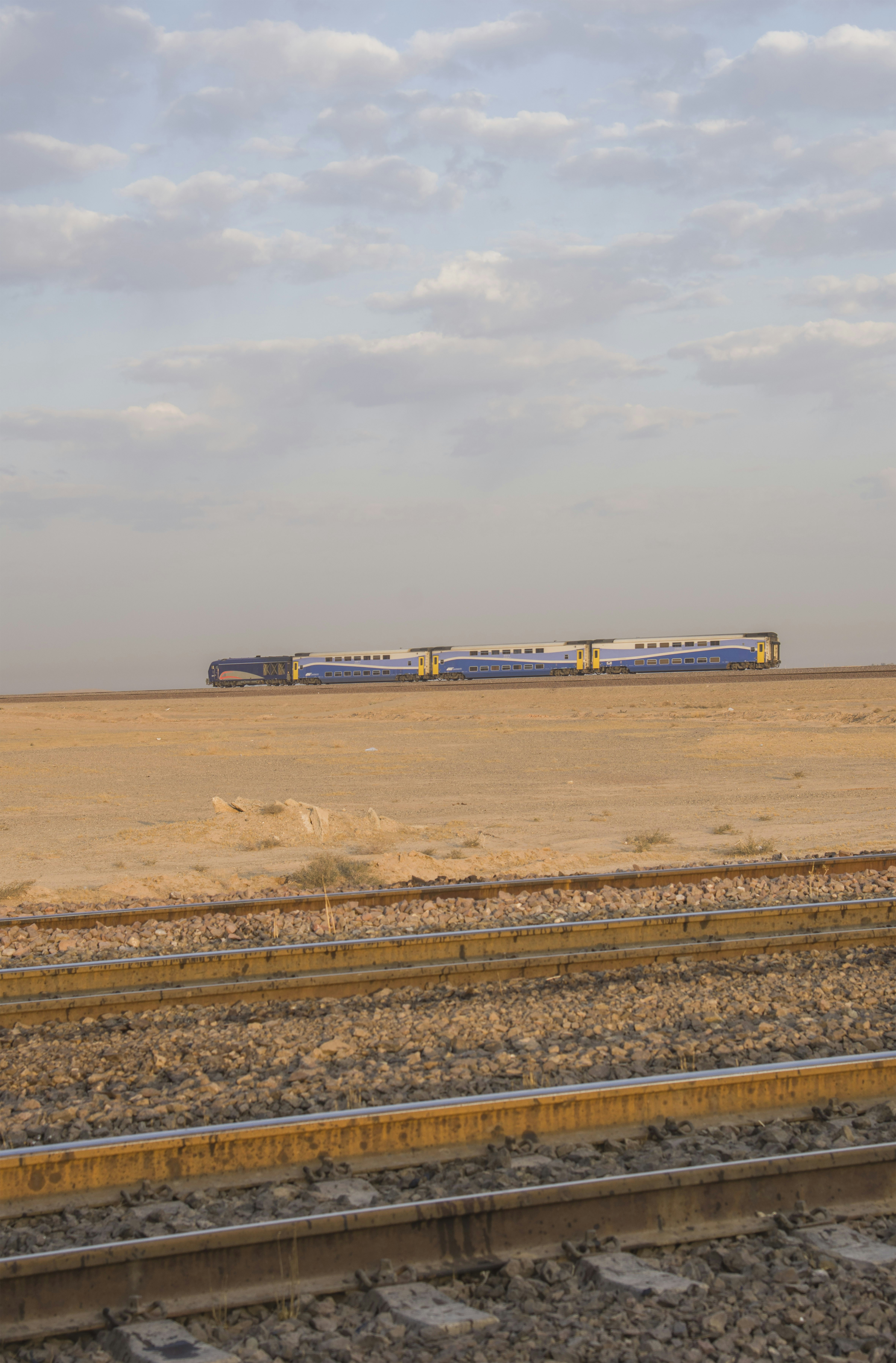A train traversing a vast, barren landscape under a cloudy sky, emphasizing the contrast between the man-made and natural environments.