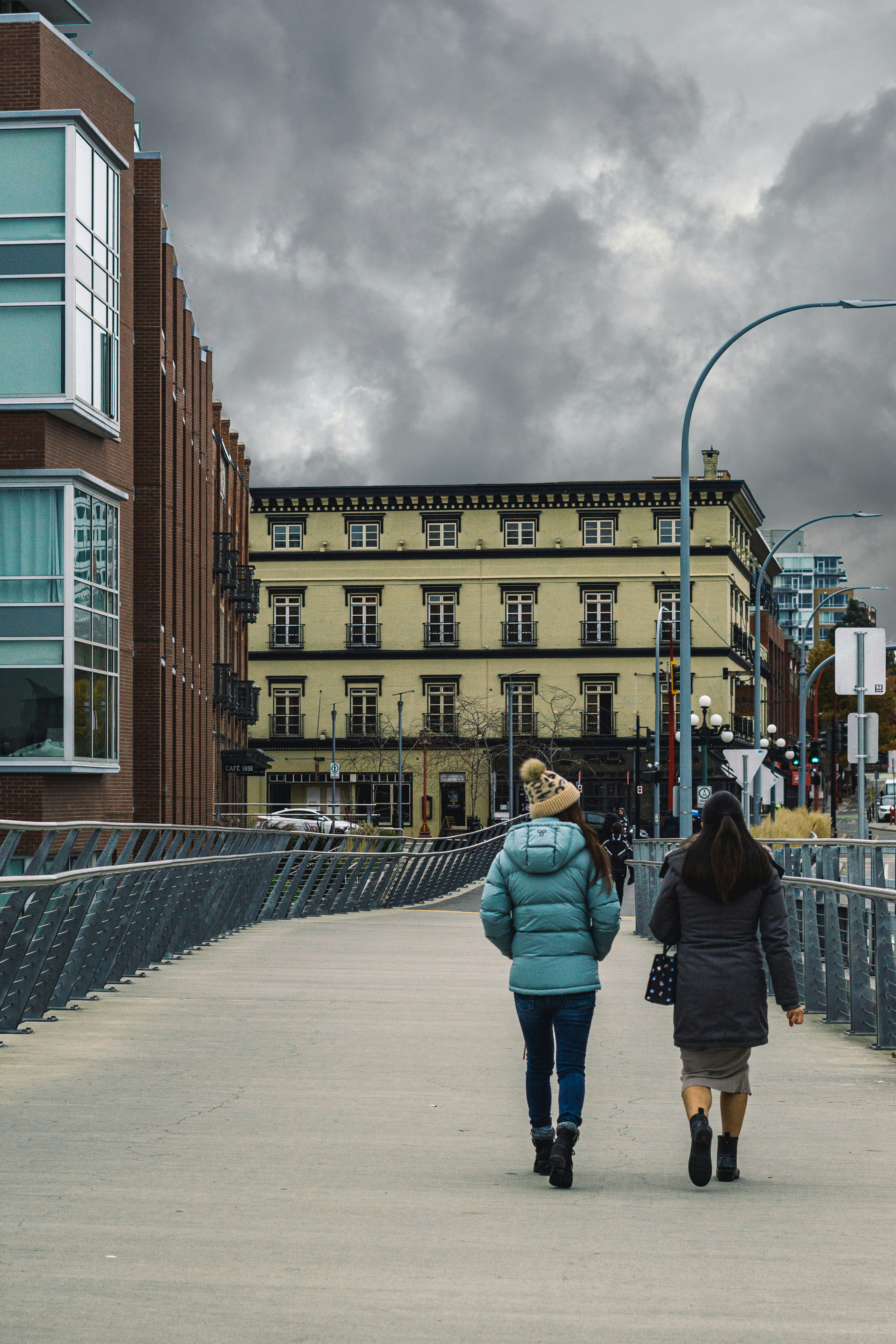 Two Wanderers on a Curved Bridge Toward a Quiet Yellow Facade