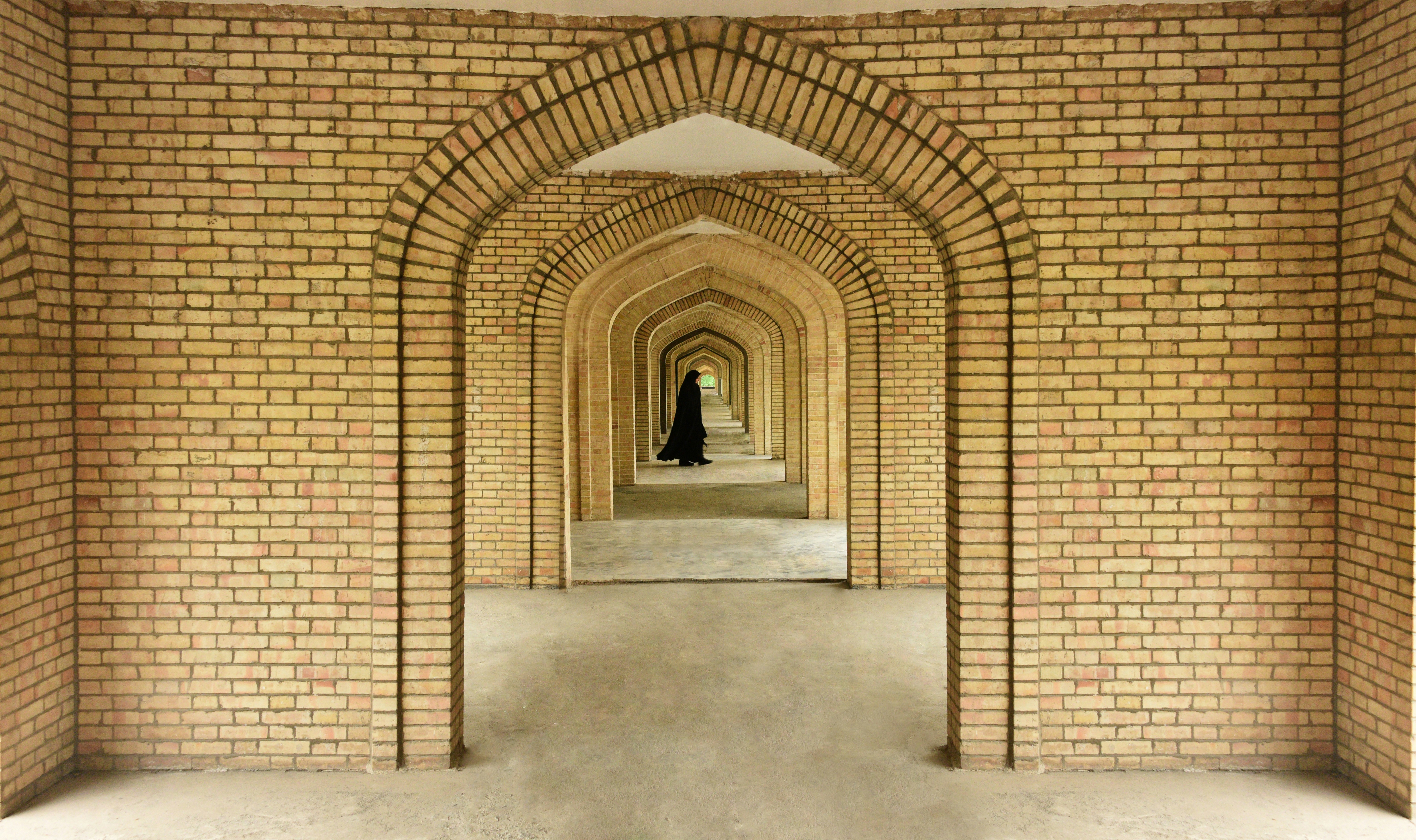 Vanishing Point Among Brick Arches: A Lone Figure at the Corridor's End