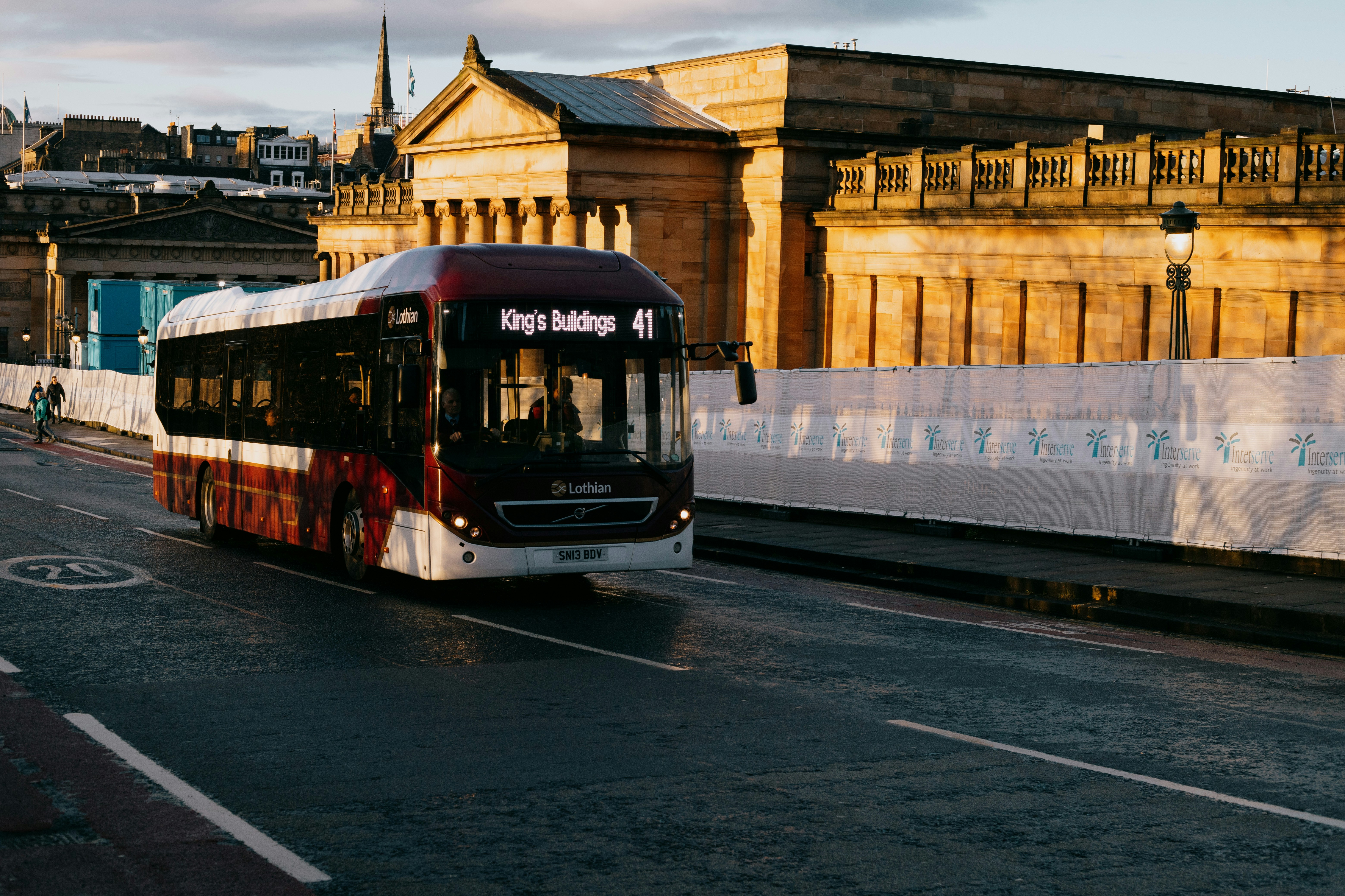 City bus traveling along a historic street, illuminated by the warm glow of the setting sun.
