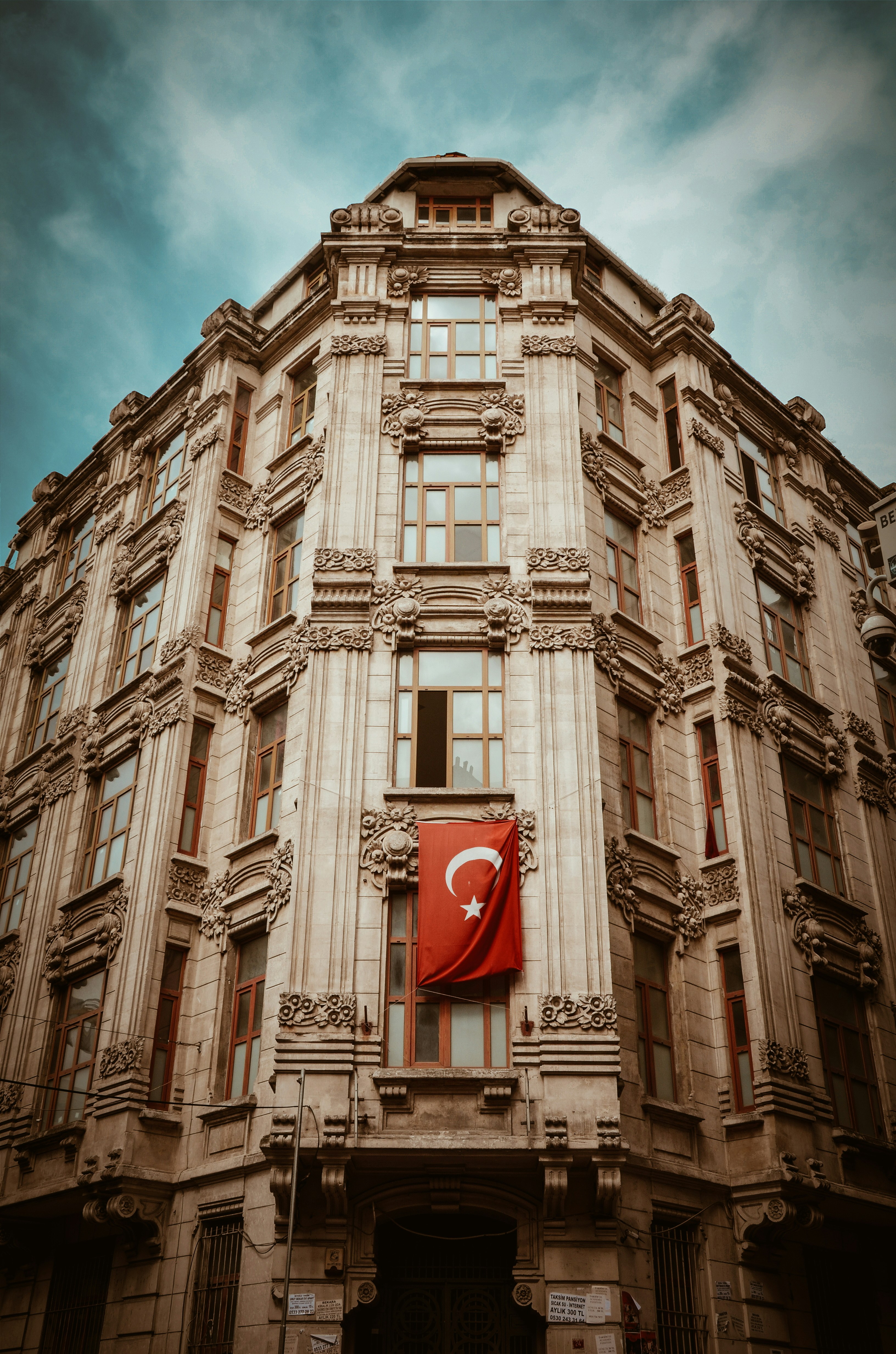 Historic building adorned with intricate architectural details, featuring the Turkish flag prominently displayed. The structure reflects a blend of cultural heritage and urban life.