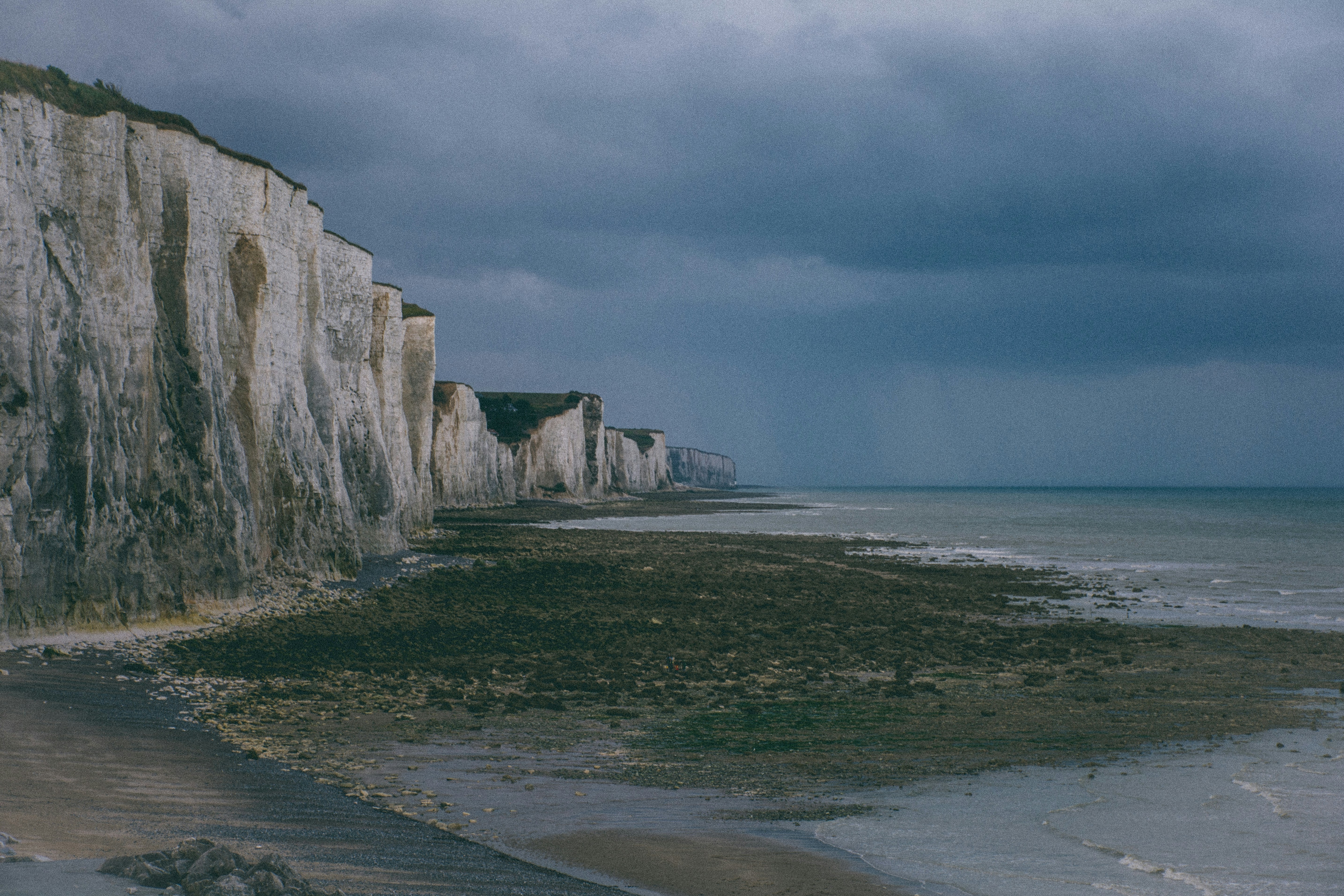 Majestic white cliffs rise dramatically against a moody sky, with a rocky shoreline revealing the relentless dance of land and sea.