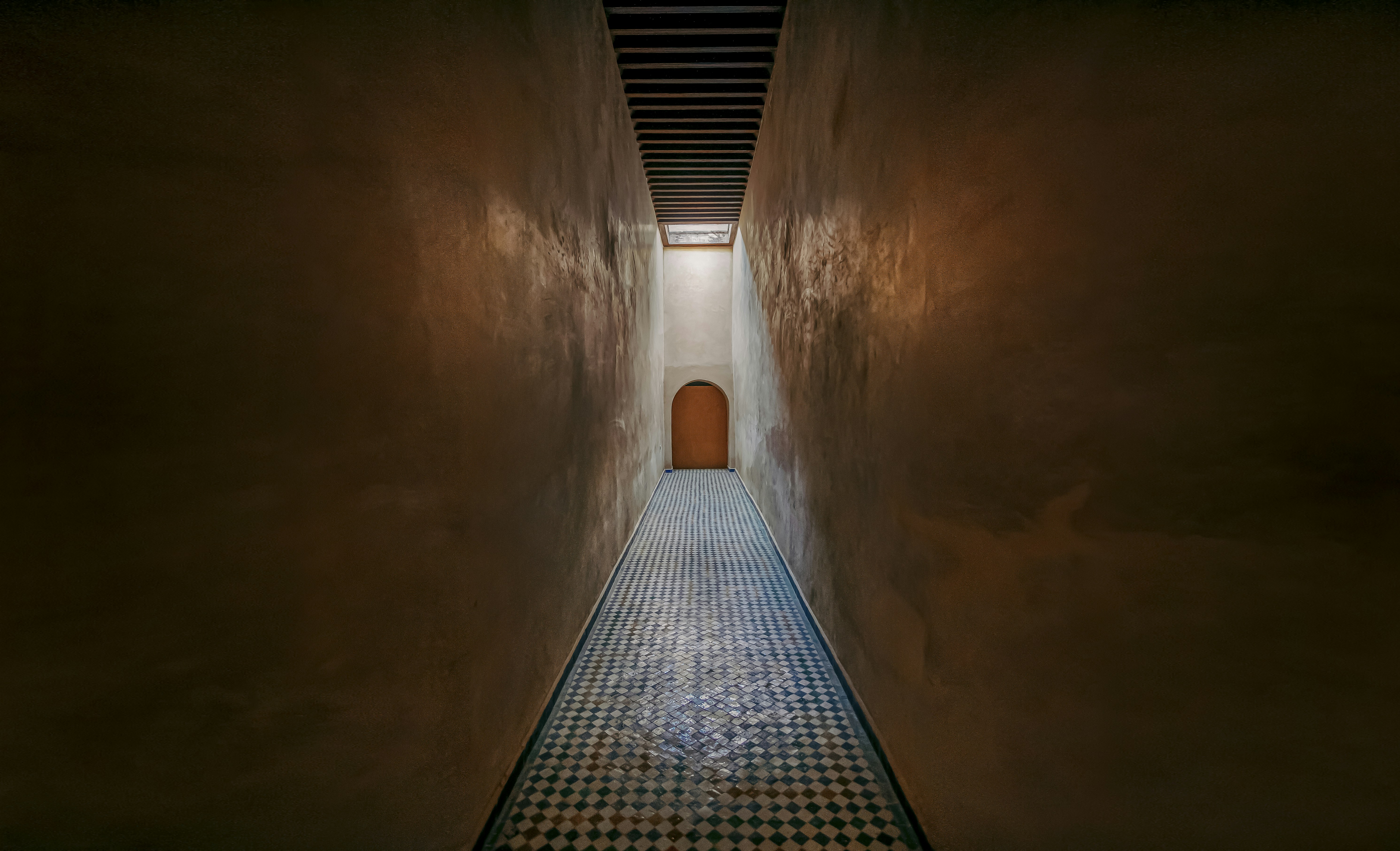 Long narrow corridor with textured walls leading to a closed wooden door under soft lighting.