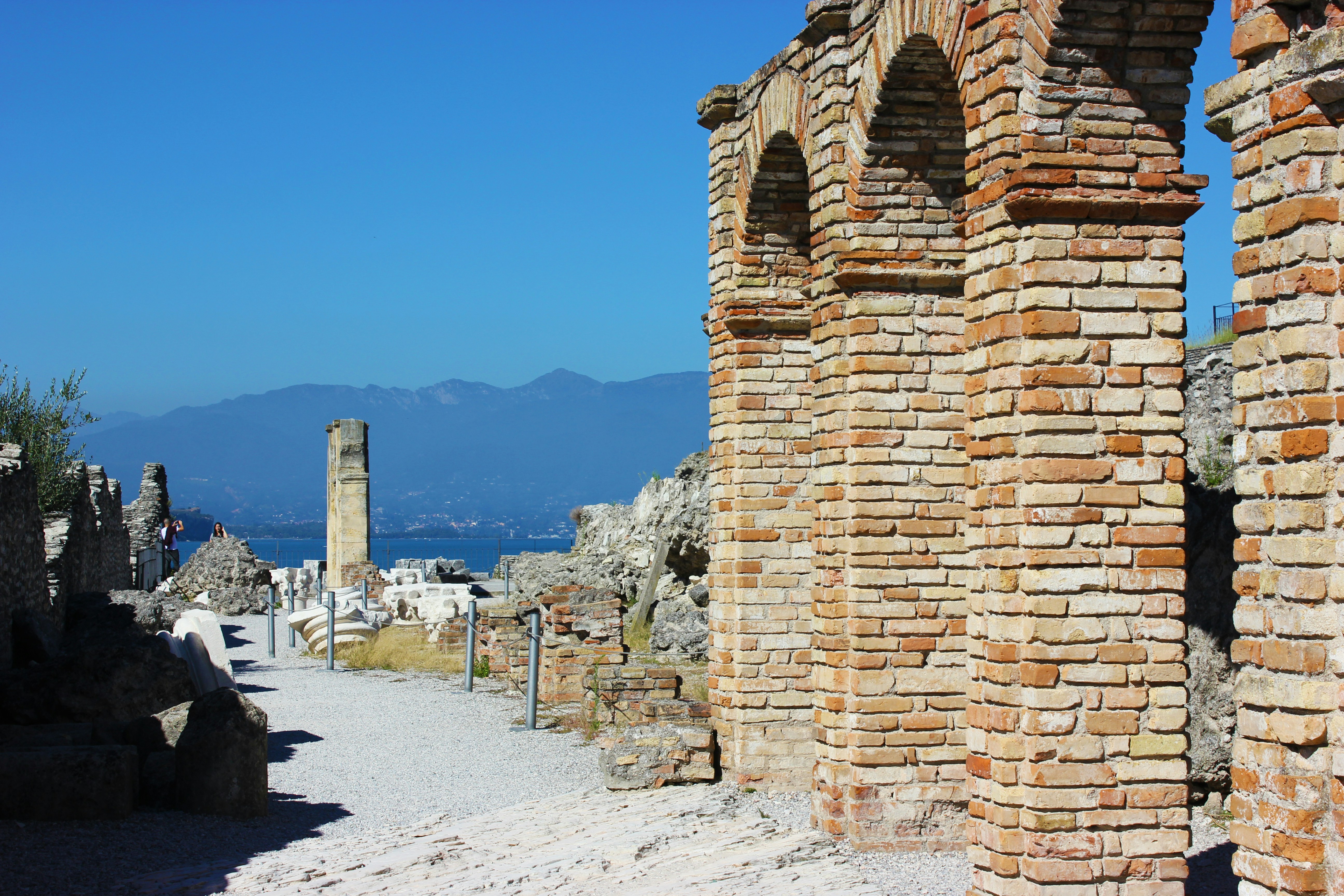 Ruins of brick arches lead the eye towards distant mountains and a serene coastline, showcasing the remnants of an ancient civilization.