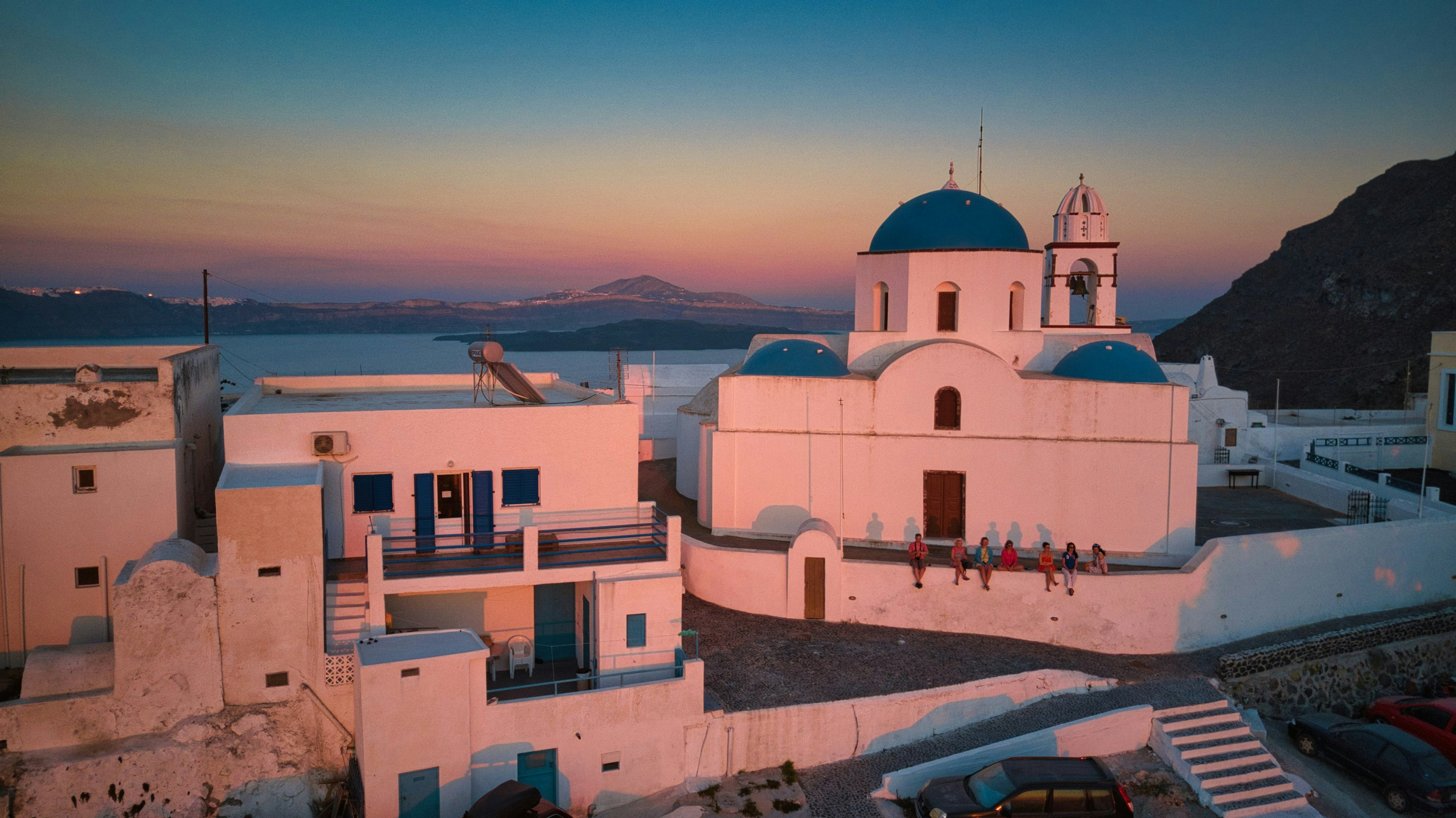 Whitewashed buildings and blue domed church at sunset on Santorini Island.
