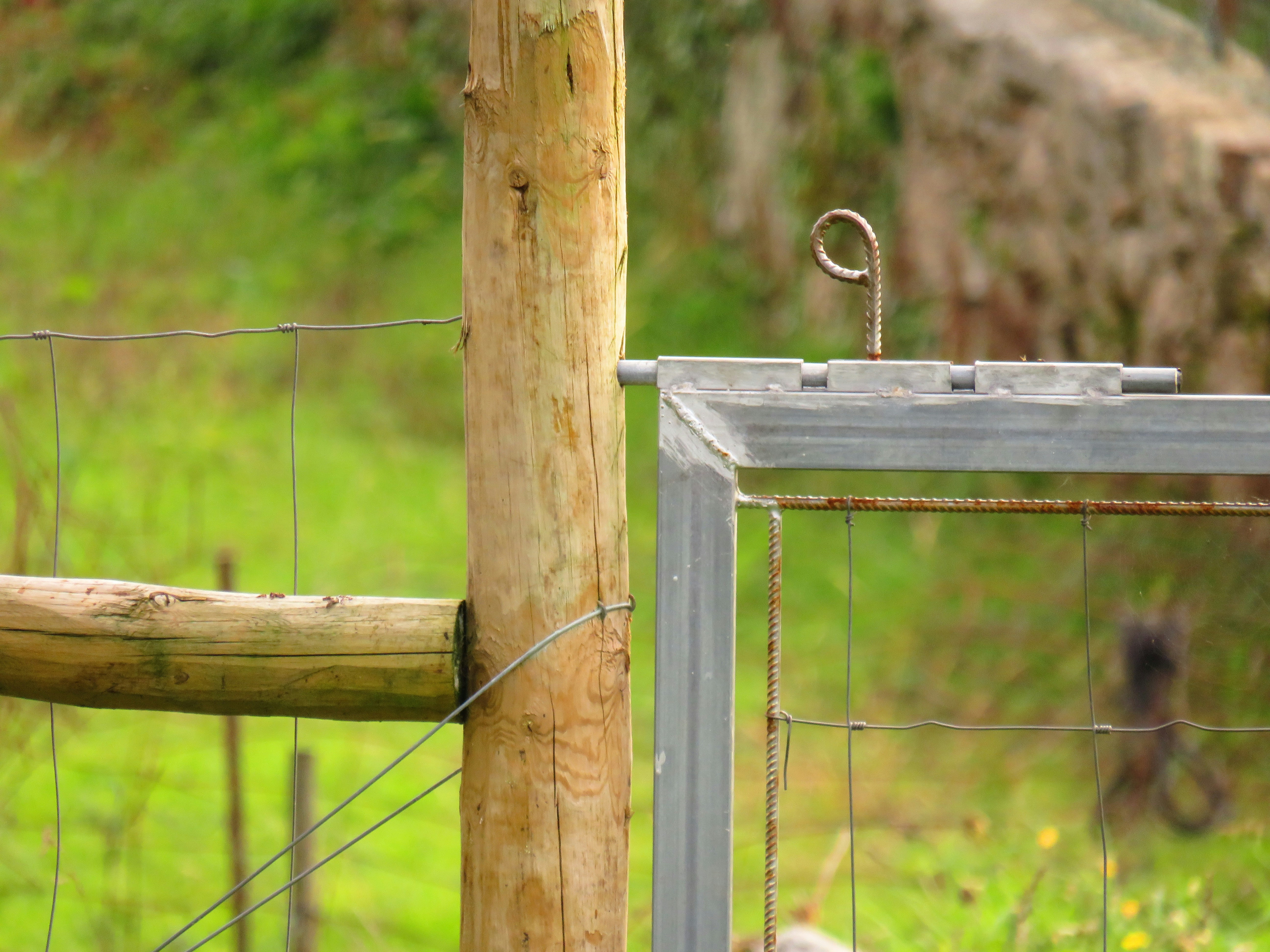 Wooden and metal fence against a lush green field with rustic textures.