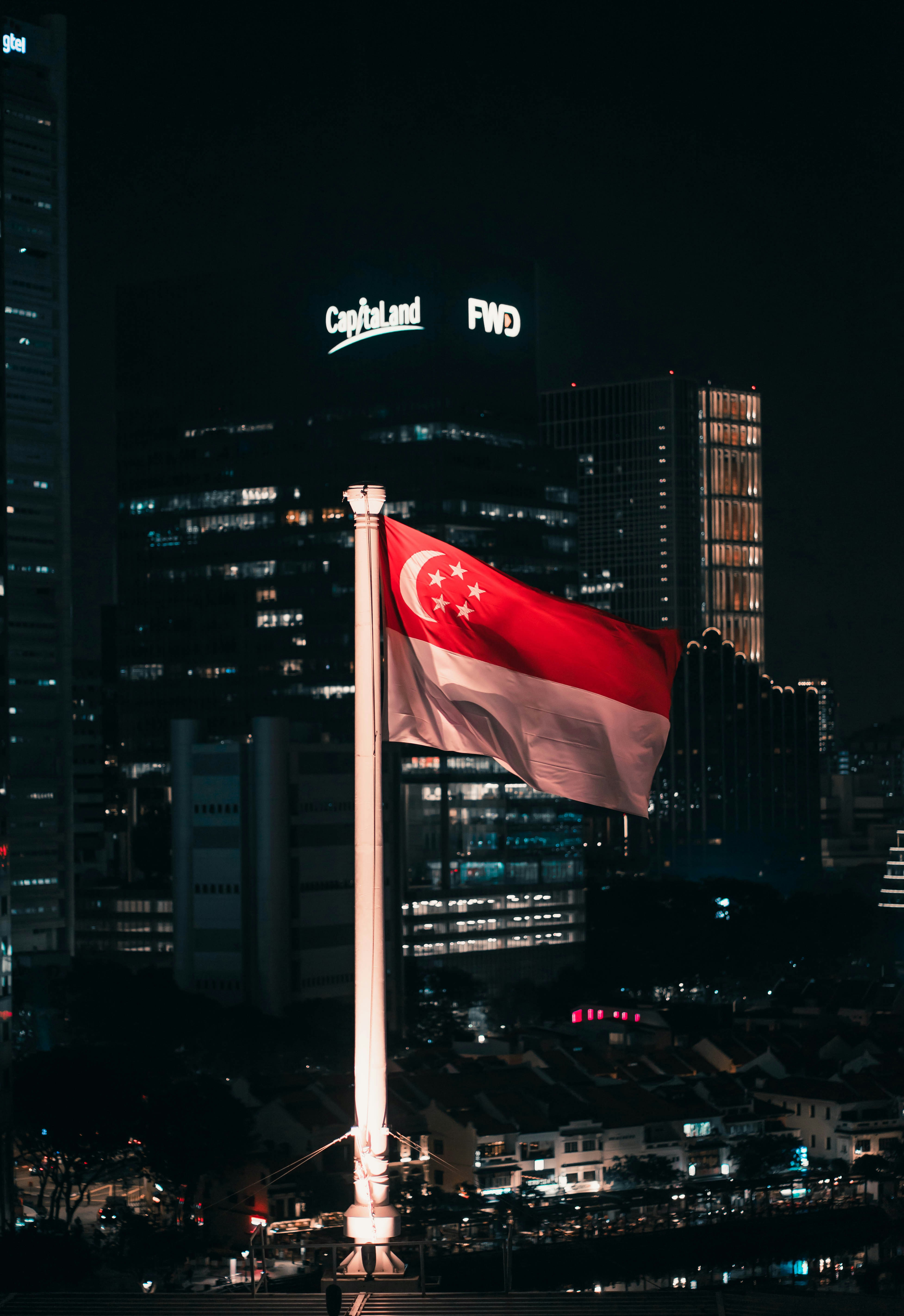 Singapore flag waving proudly against a backdrop of illuminated skyscrapers at night.
