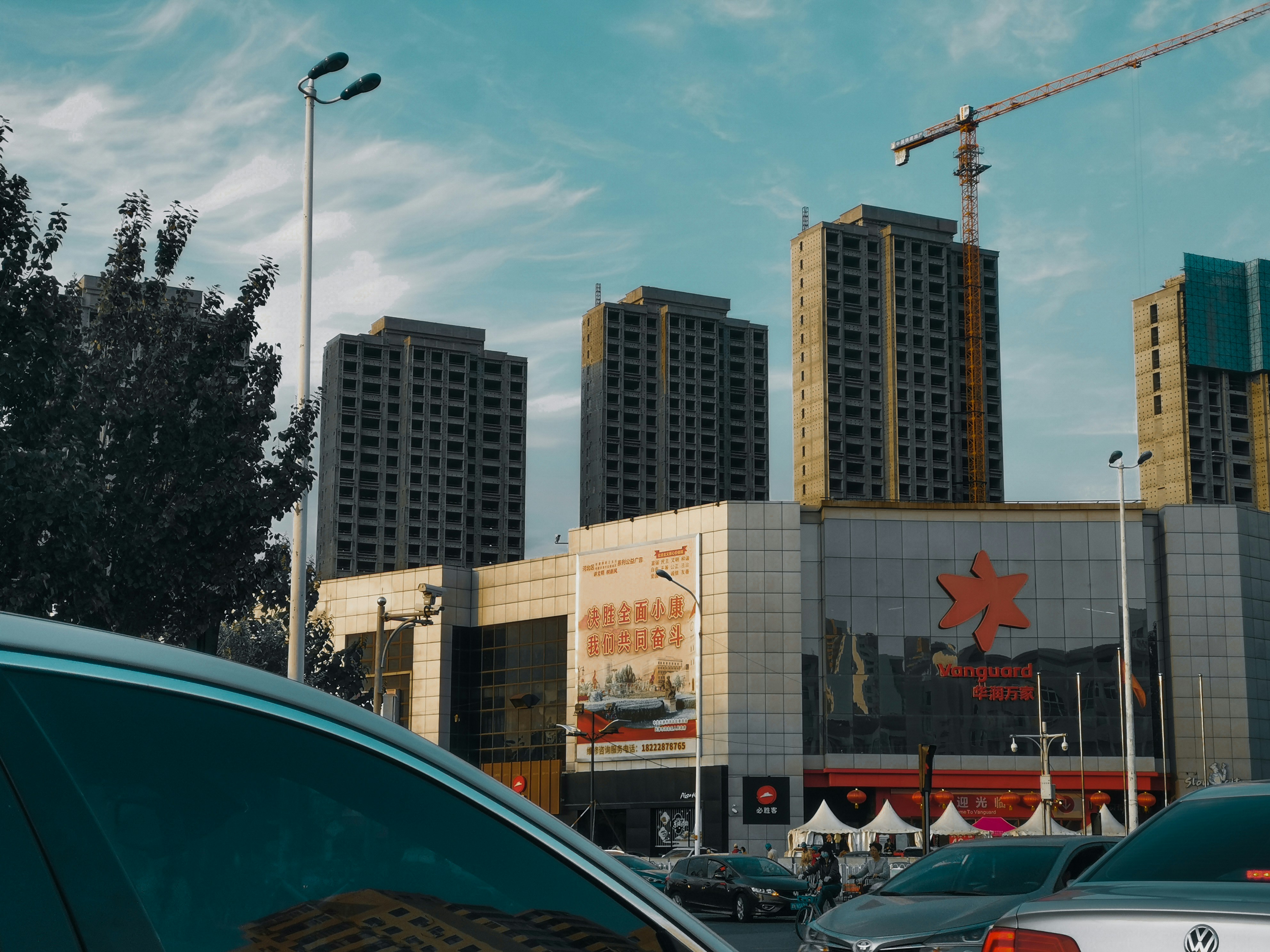 Modern shopping-center facade featuring a bold red star logo rises above a busy city street, with a curved blue car in the foreground.