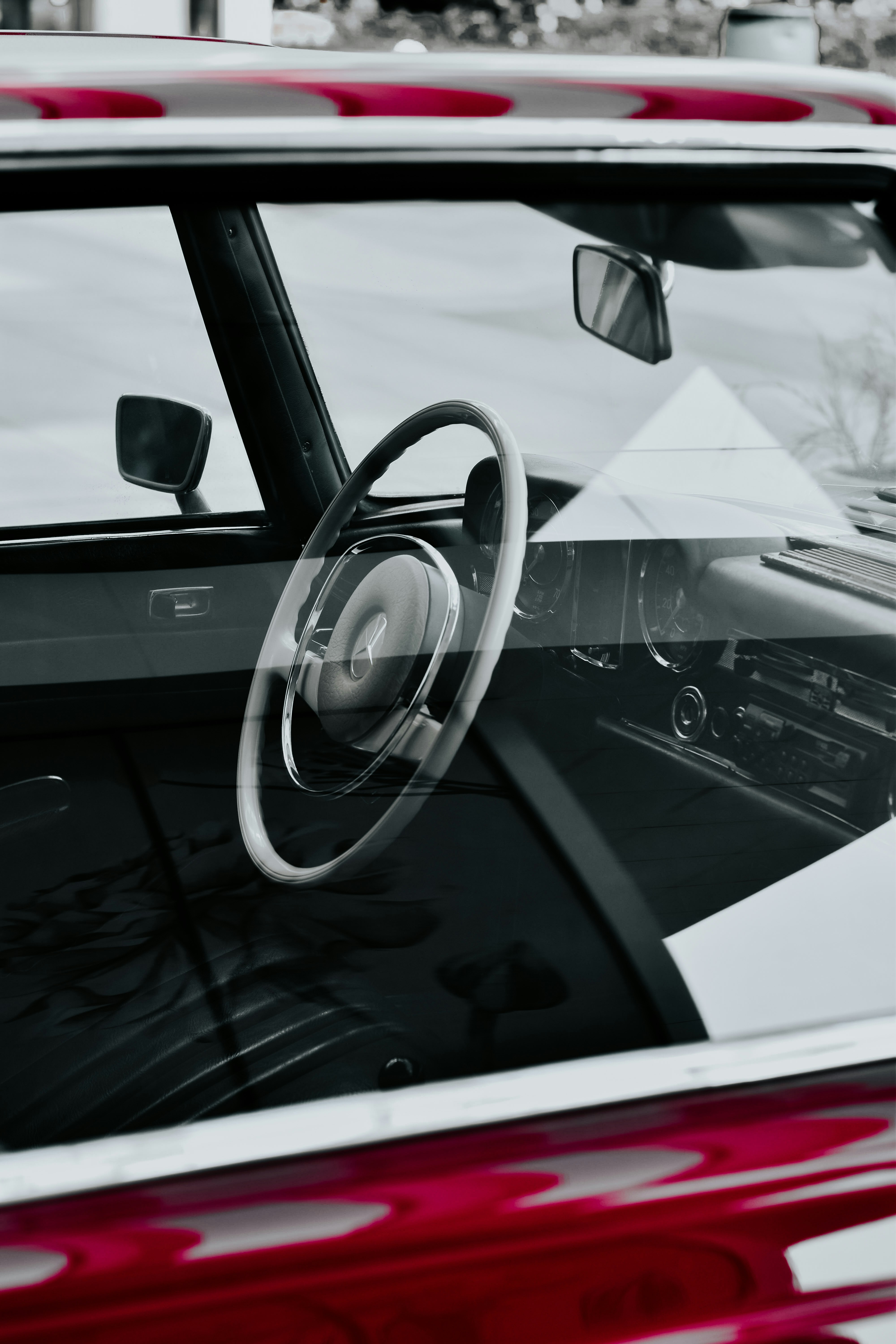 Quiet Focus: A Classic Car's Circular Steering Wheel Framed by Glass and Chrome Reflections