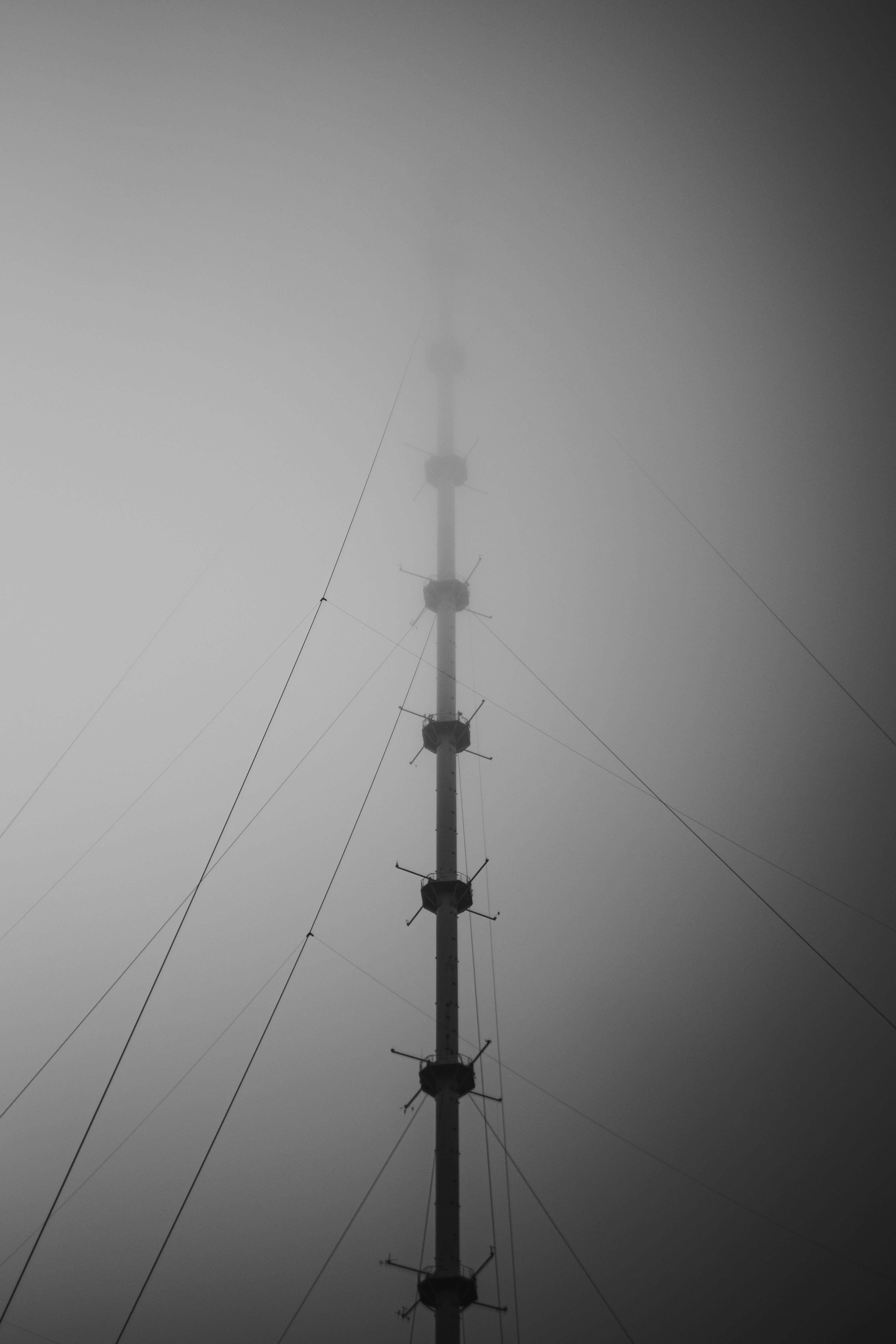 A tall communication tower emerges from dense fog, its structure partially obscured, creating a sense of mystery and isolation.