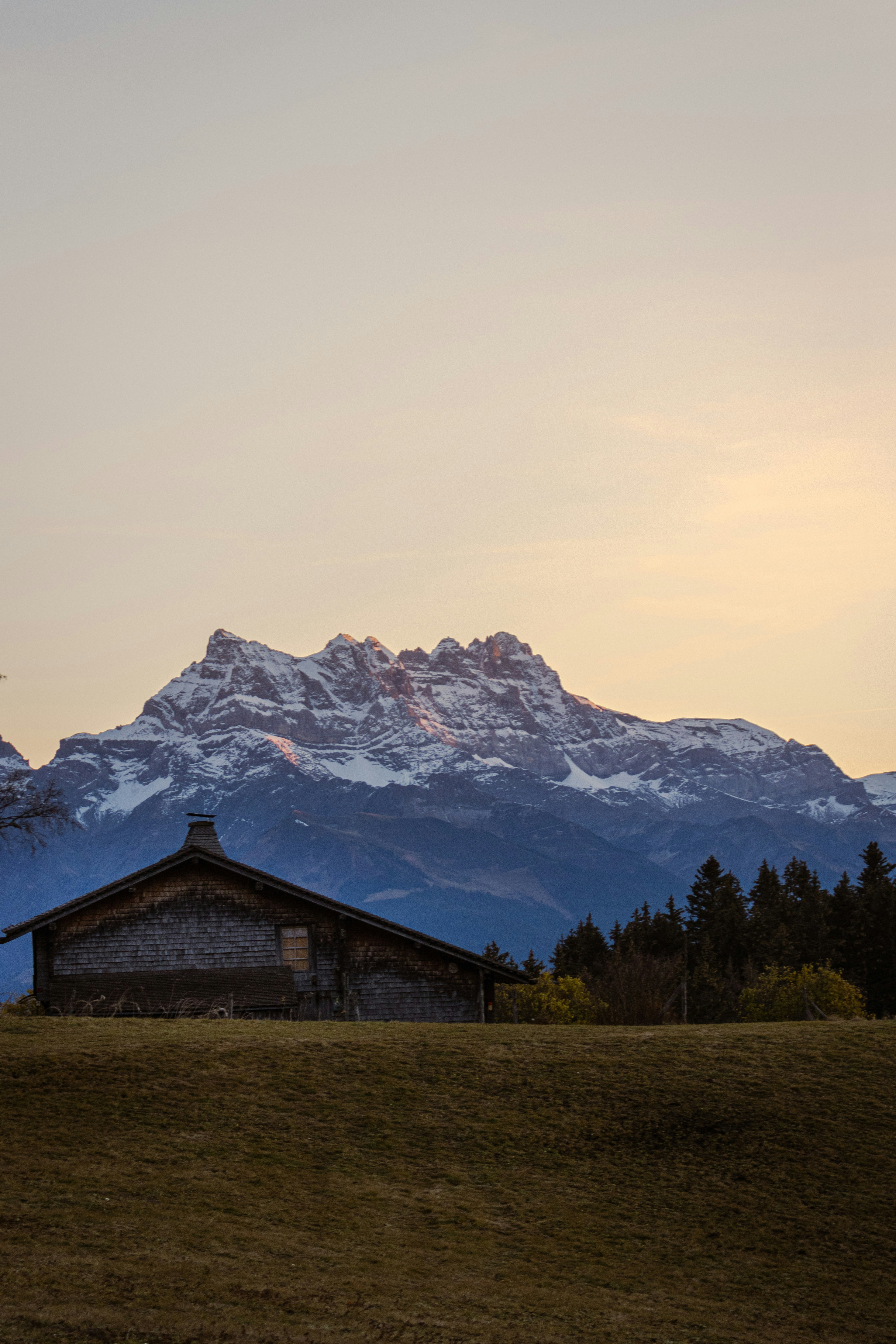 A rustic wooden cabin set against the majestic backdrop of snow-capped mountains at twilight, highlighting the serene beauty of nature.