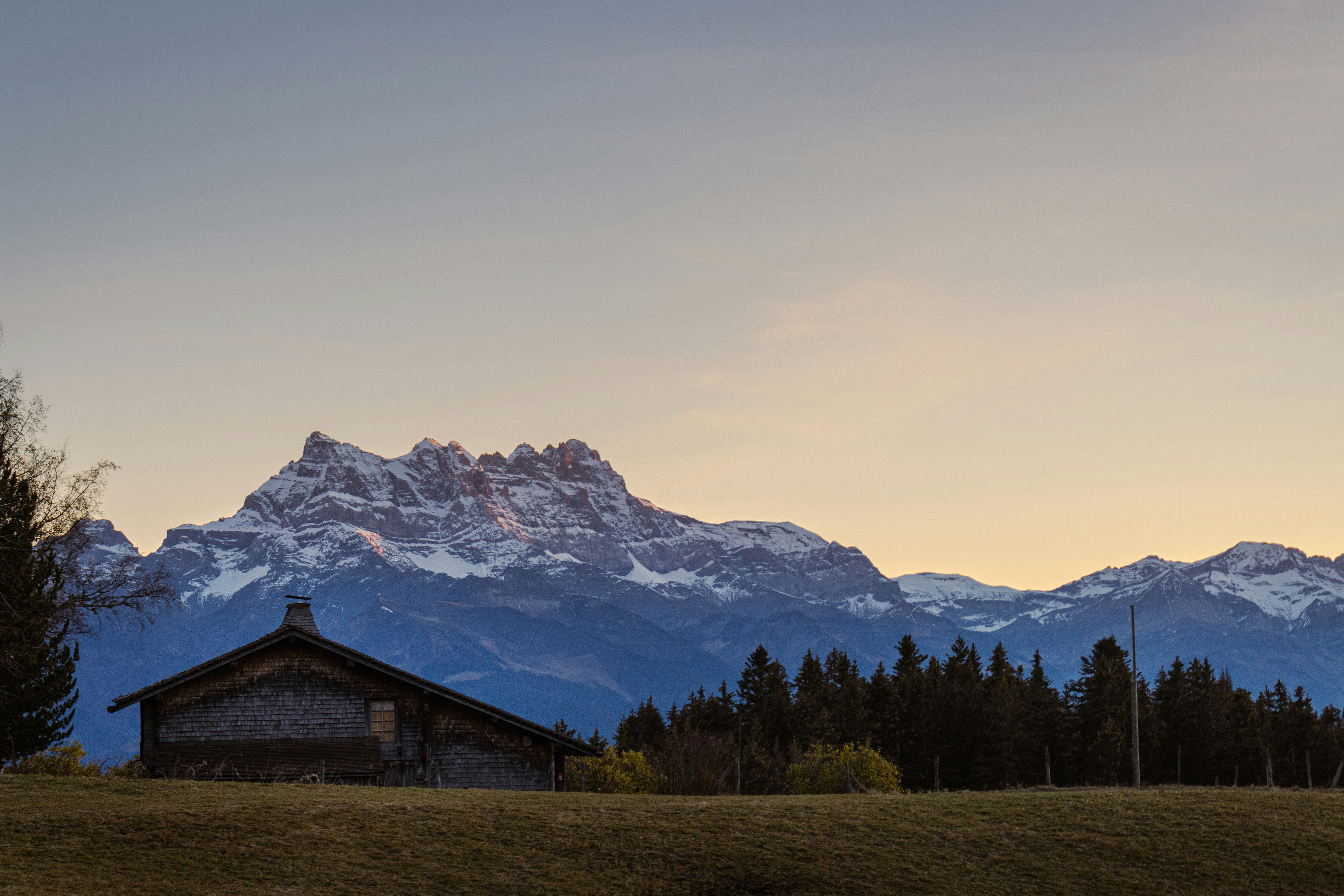 A rustic cabin nestled in a serene landscape, framed by majestic snow-capped mountains at dusk.
