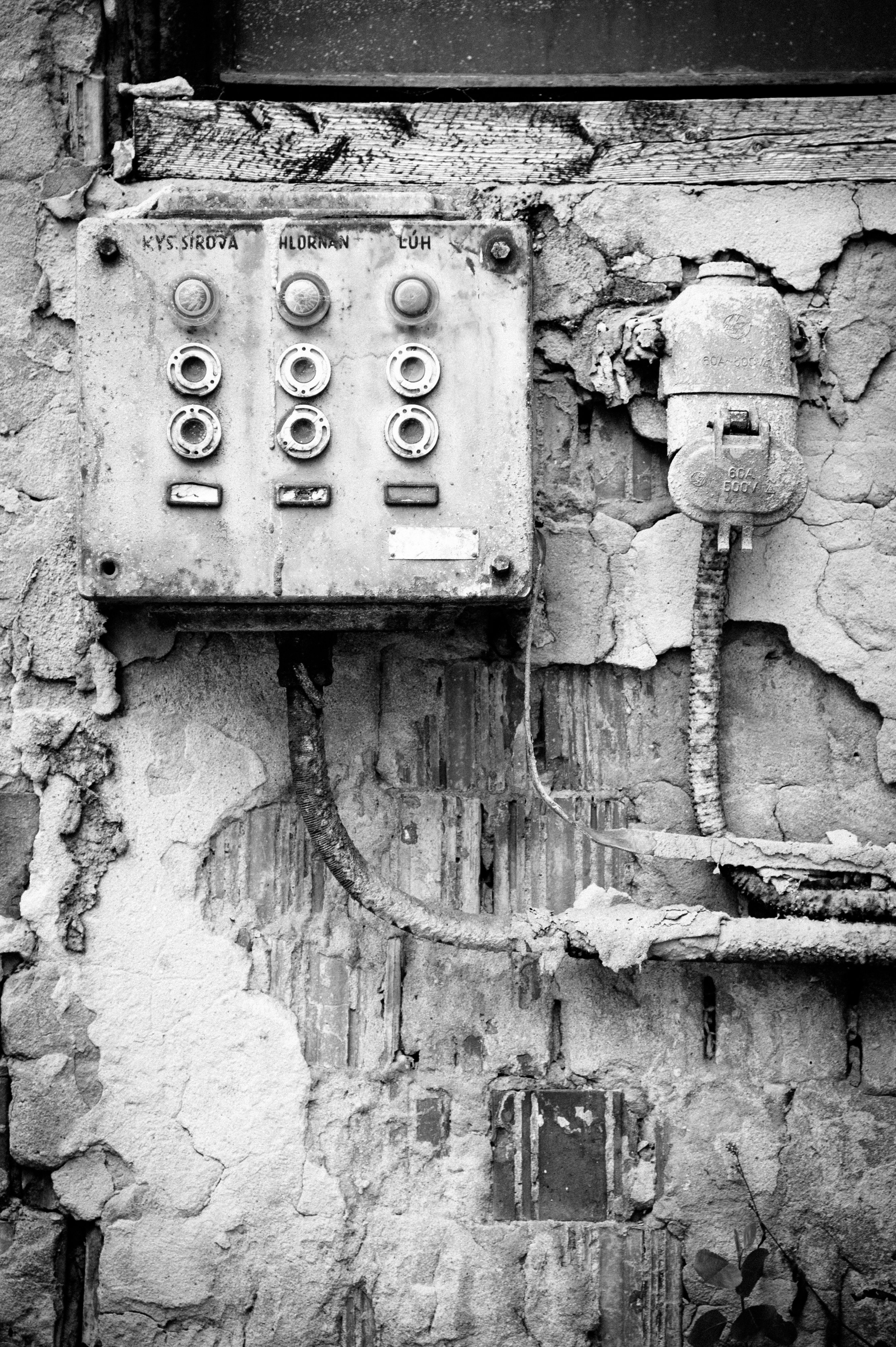 Weathered control panel mounted on a cracked wall, showcasing vintage buttons and electrical connections.