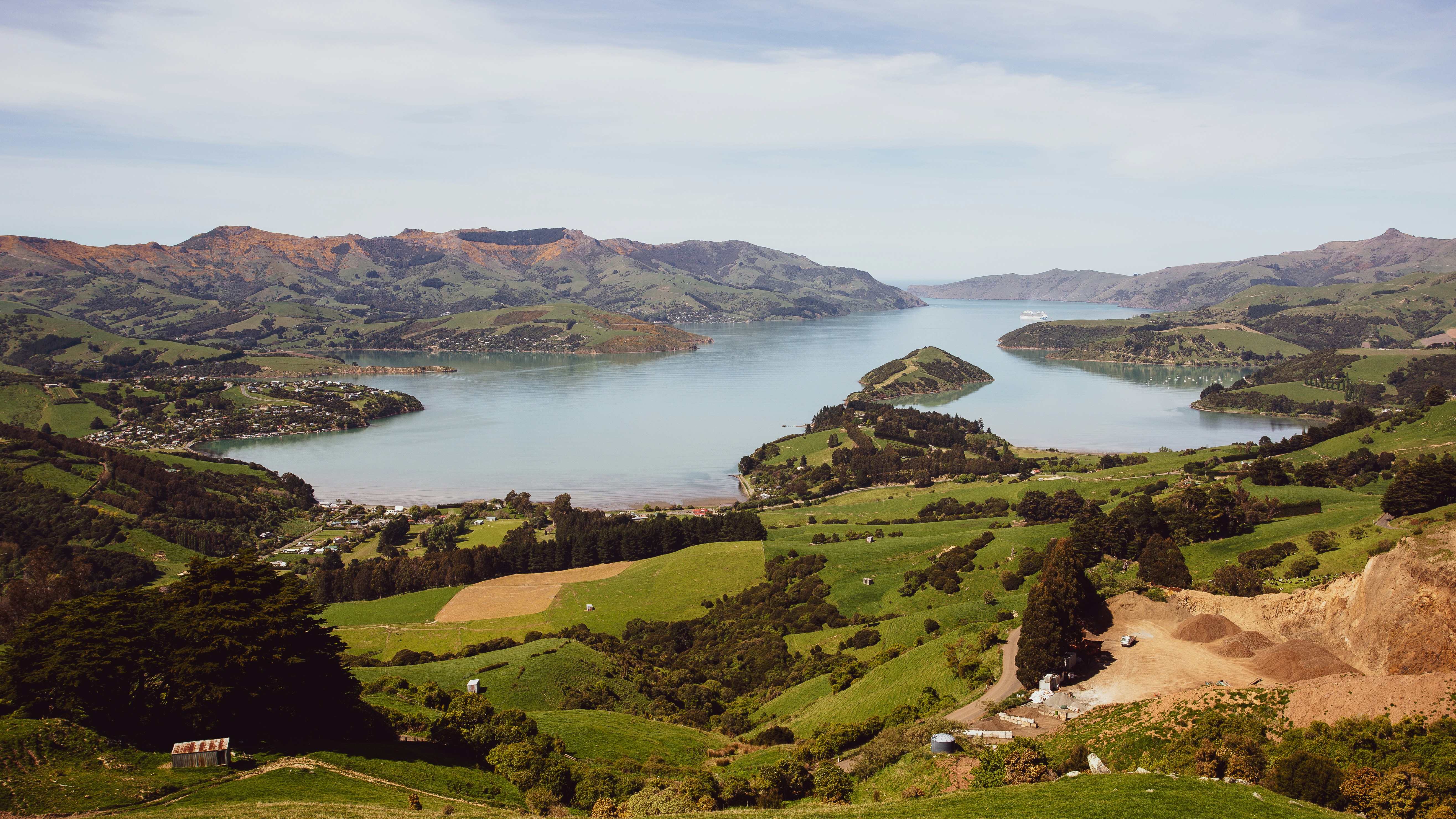 Vibrant green hillsides frame a serene bay, reflecting the sky's soft hues. The landscape showcases a harmonious blend of nature's beauty and tranquility.