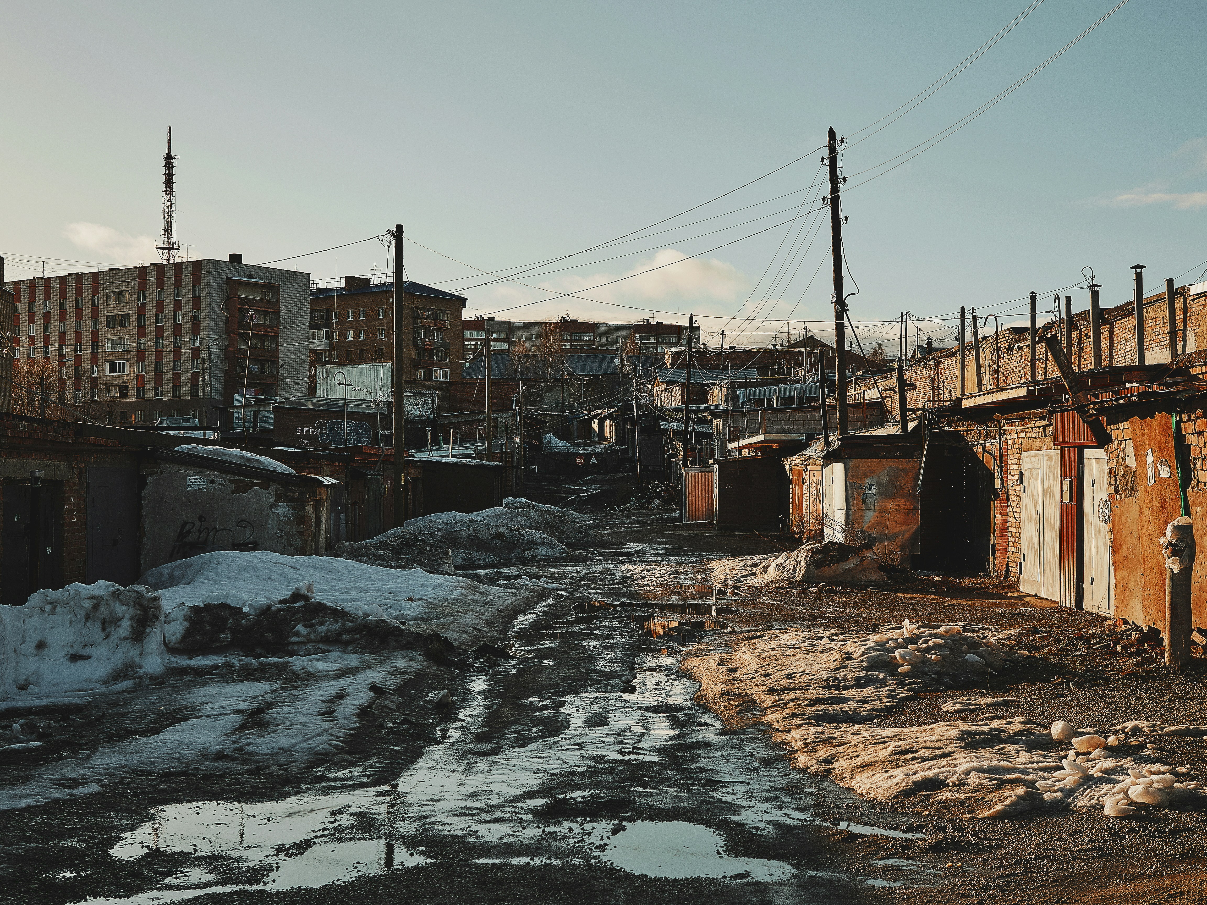Abandoned alleyway lined with dilapidated structures and remnants of snow, reflecting the harshness of urban life.