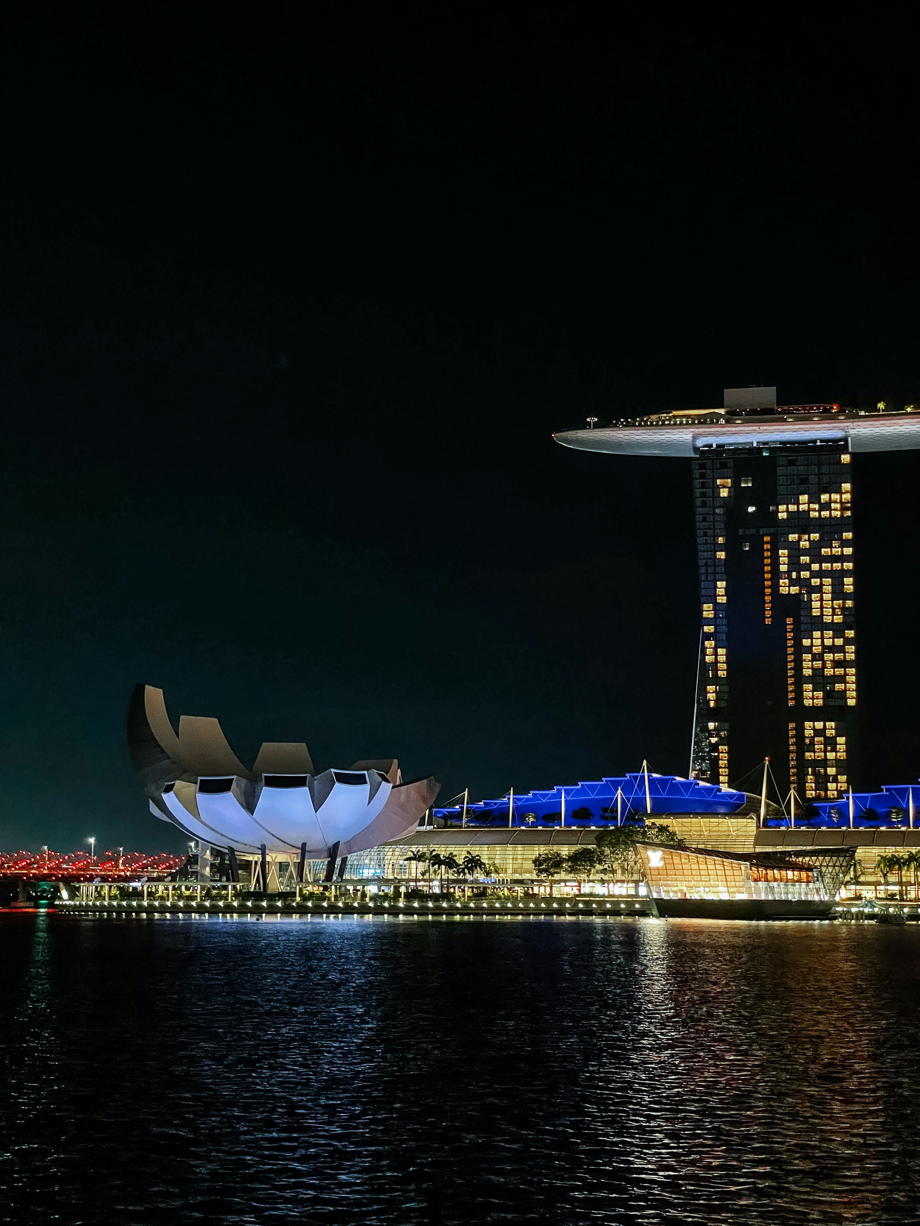 Futuristic building complex illuminated against the night sky, showcasing modern design elements and vibrant colors reflected on water.