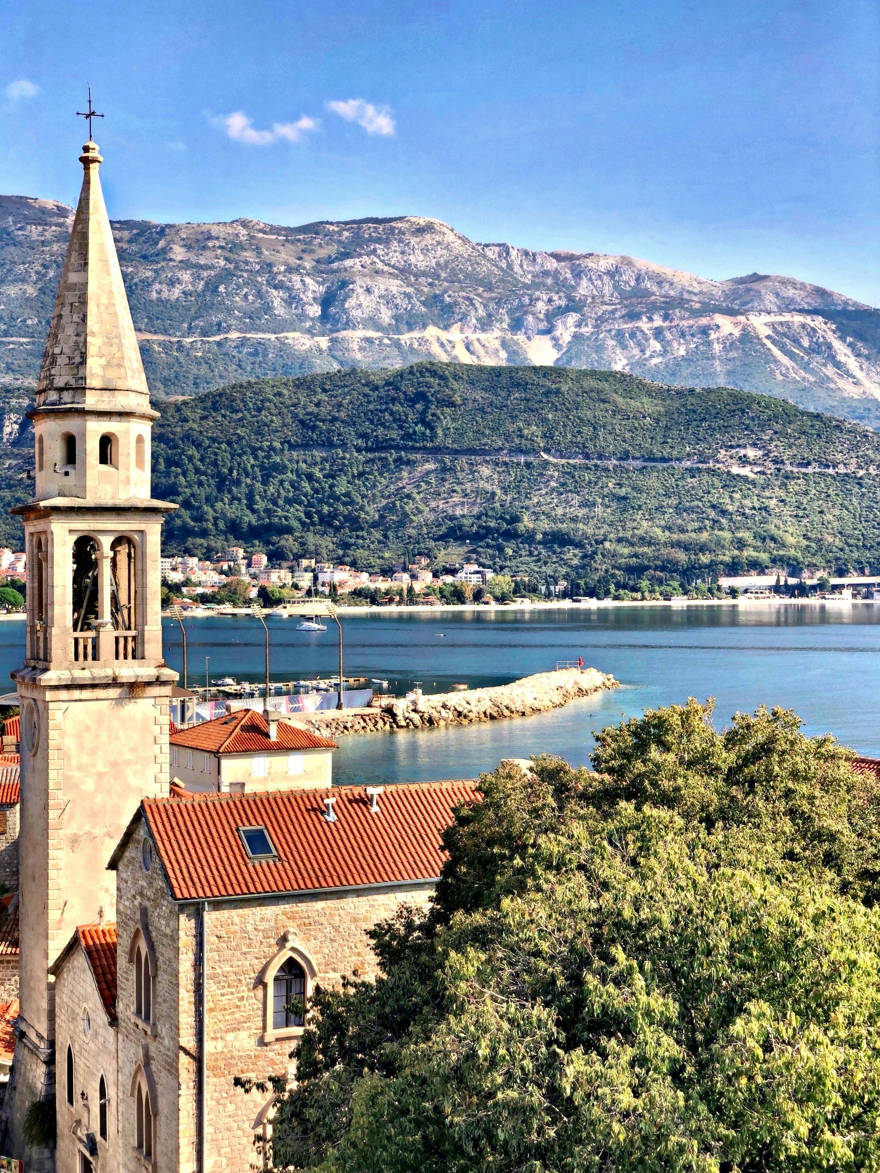 Historic church tower alongside a tranquil bay, framed by lush greenery and distant mountains.