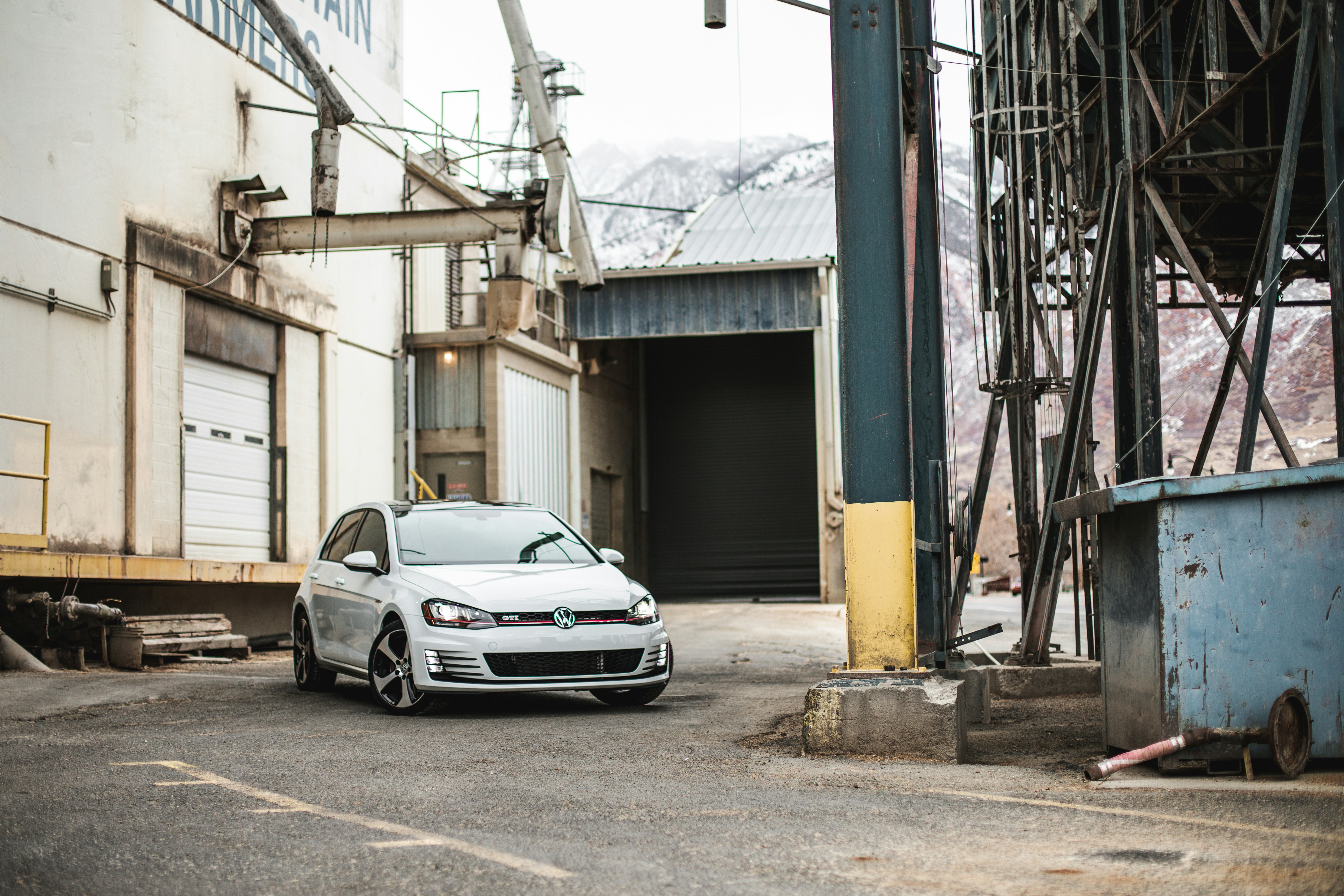 A sleek silver hatchback parked in an industrial area, framed by weathered buildings and machinery. The scene captures a blend of urban life and automotive design.