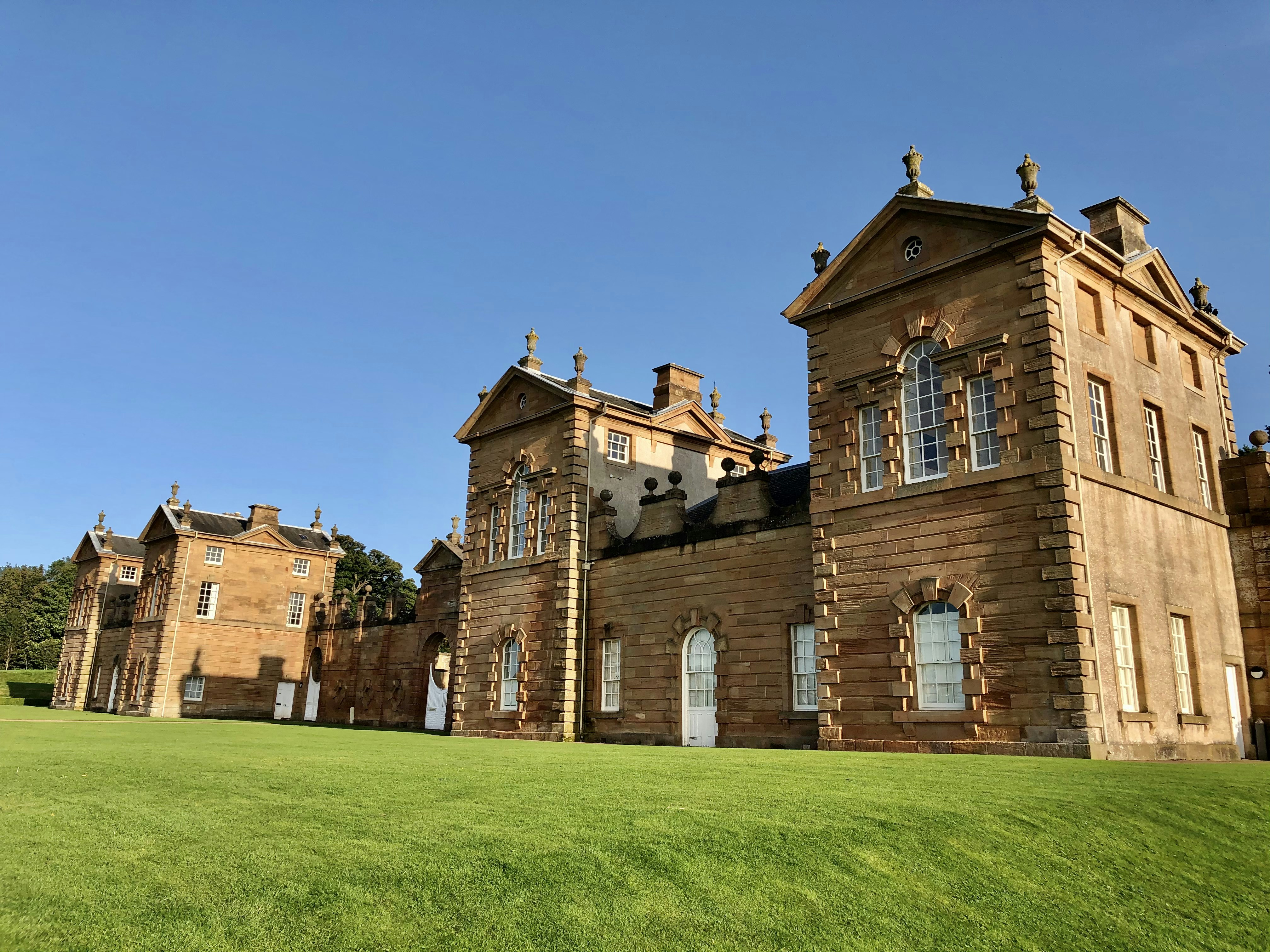Ornate brown stone manor set against a vibrant green lawn under a clear blue sky.