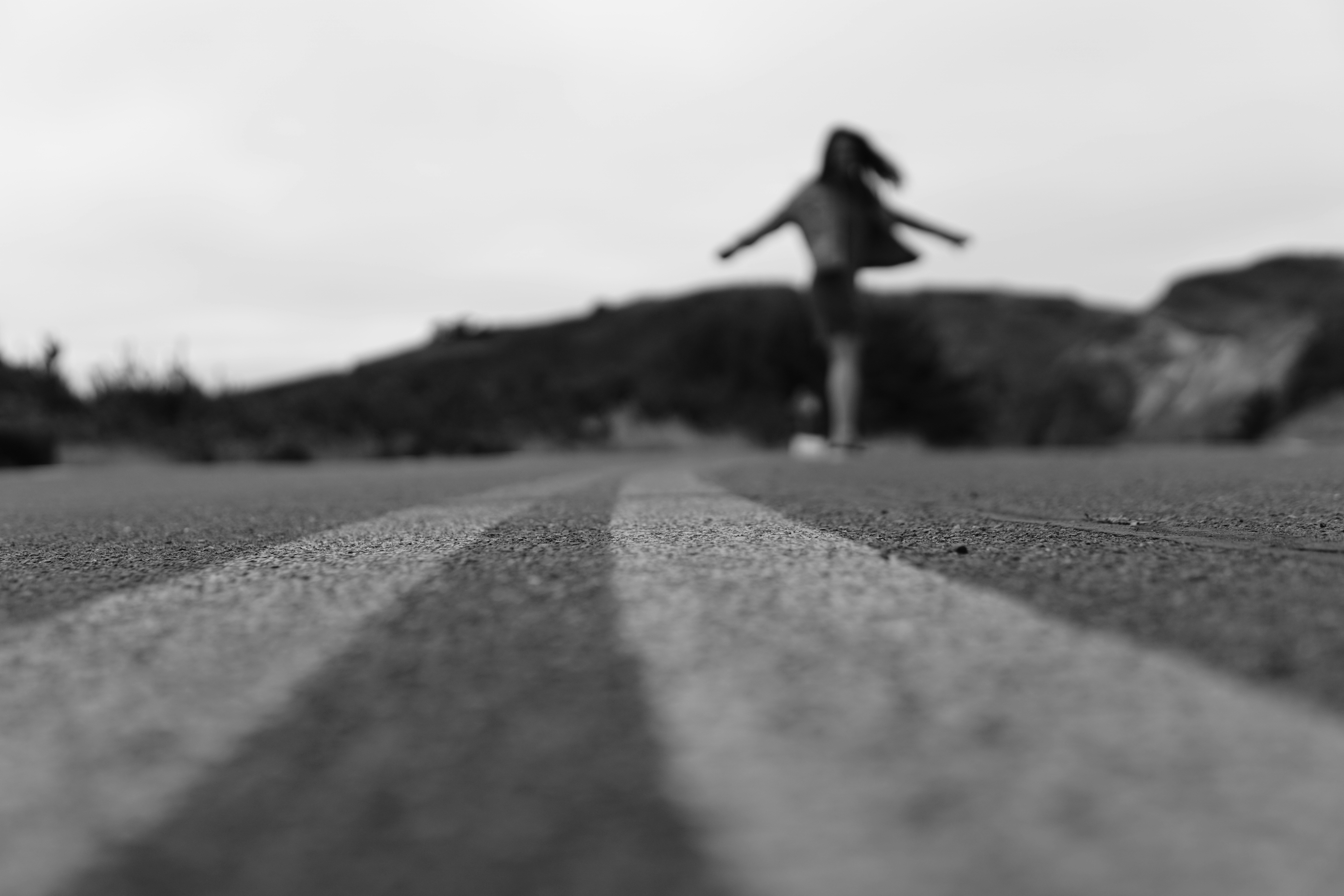 A figure joyfully twirls on a deserted road, framed by distant hills, captured in striking black and white.