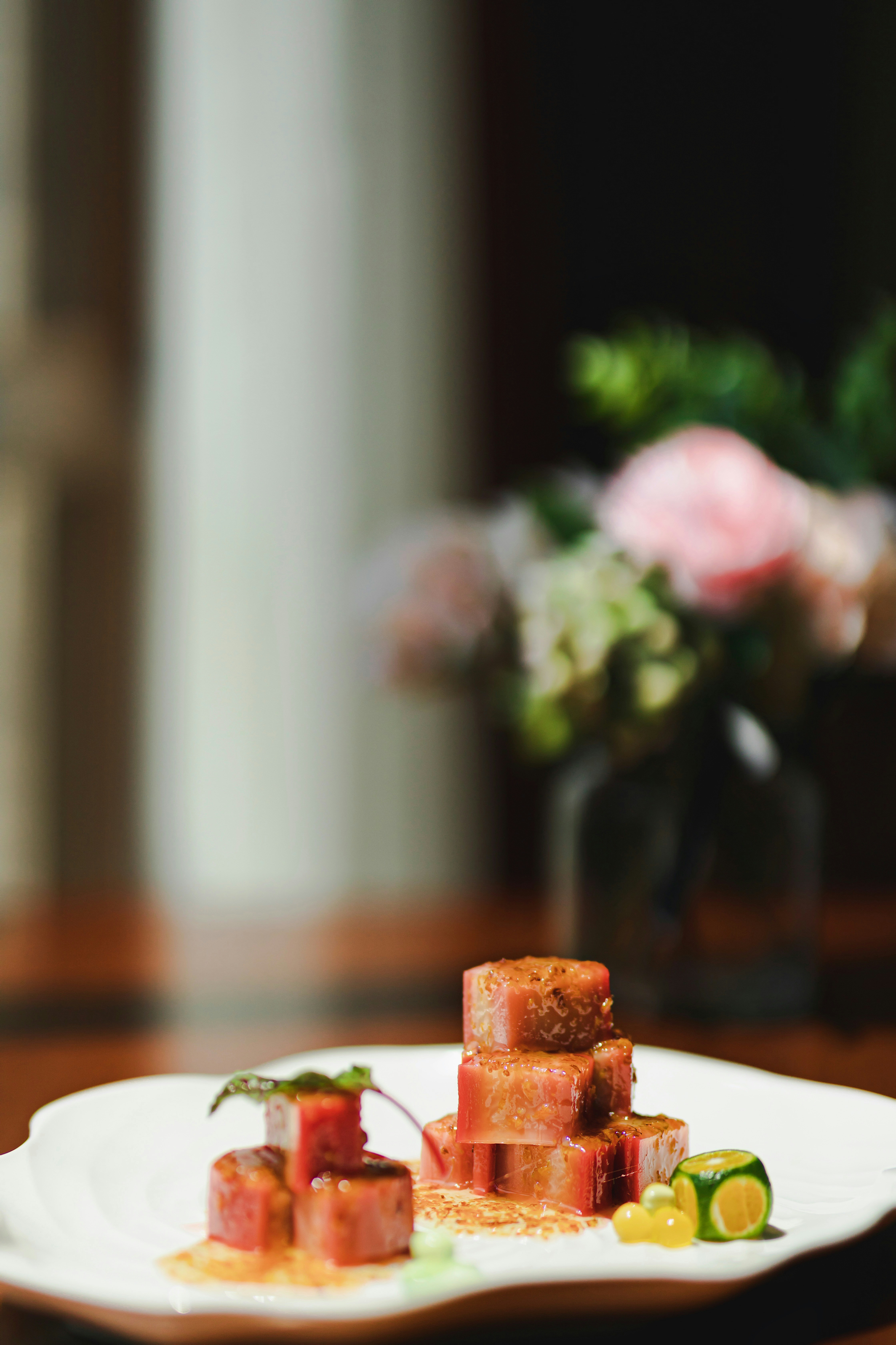 Citrus-glazed meat cubes stacked on a plate, framed by a soft floral backdrop