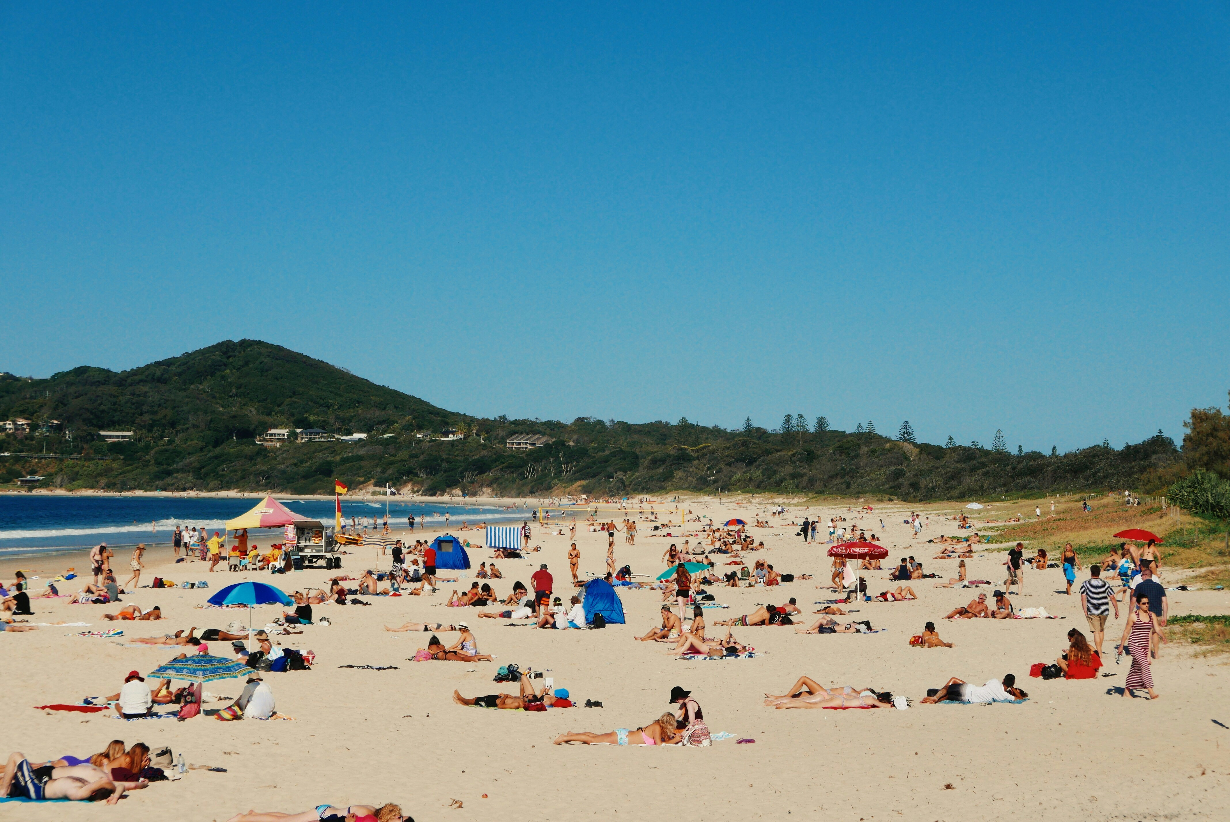 Vibrant beach scene bustling with sunbathers, colorful umbrellas, and gentle waves under a clear blue sky.