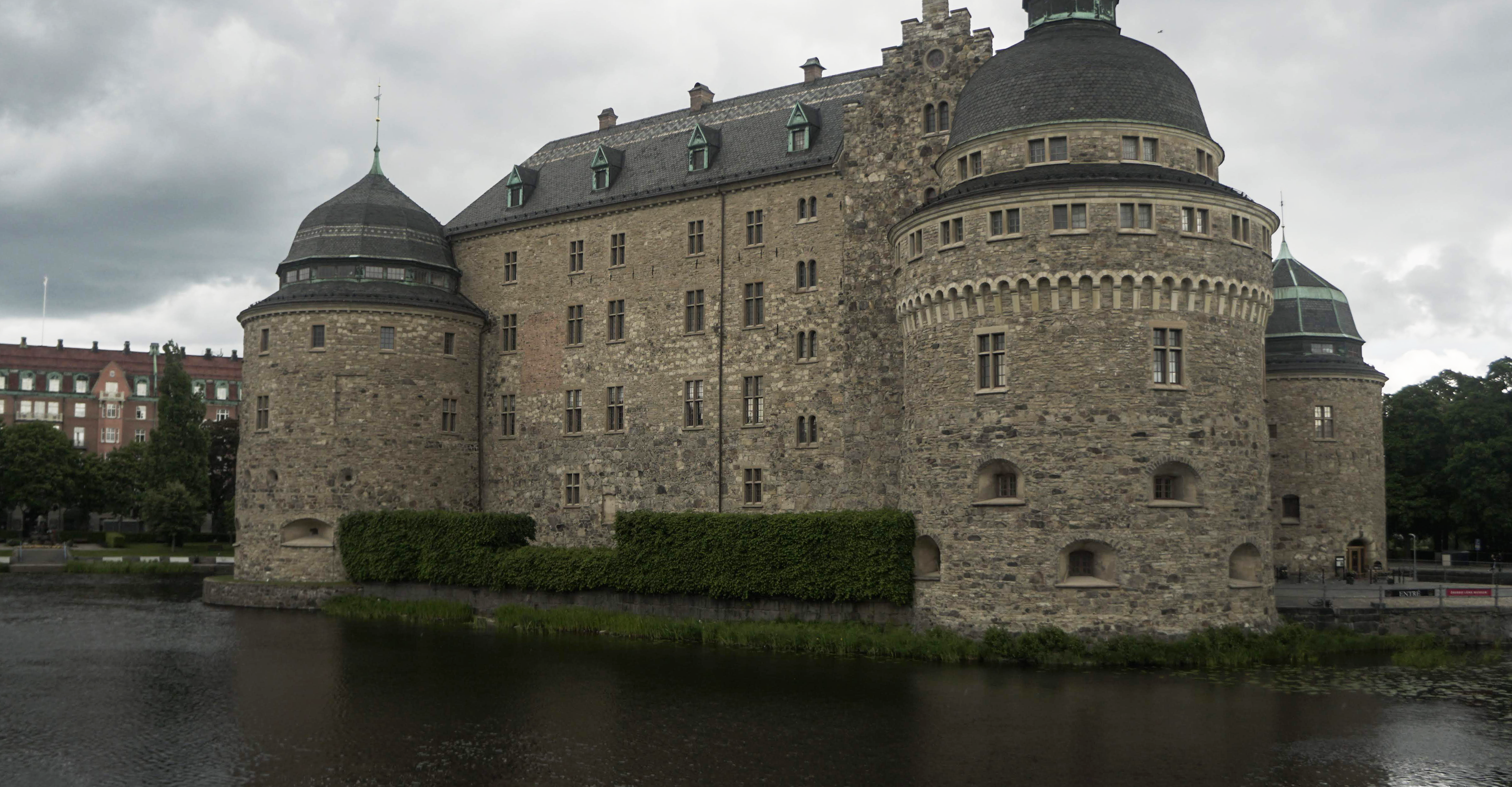 Historic stone castle with round towers and a moat under a cloudy sky.