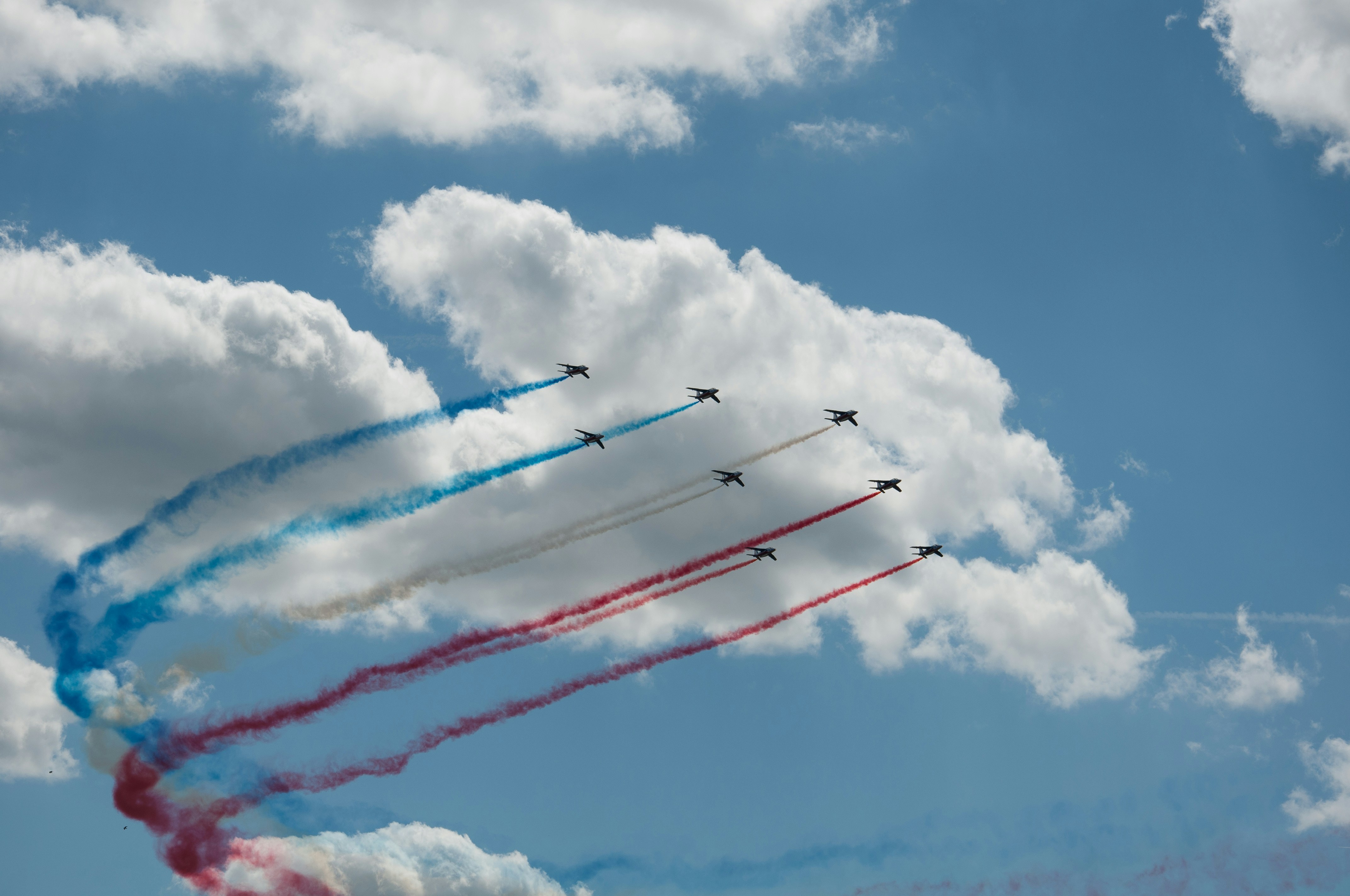 Fighter planes trailing colorful smoke against a backdrop of fluffy clouds.