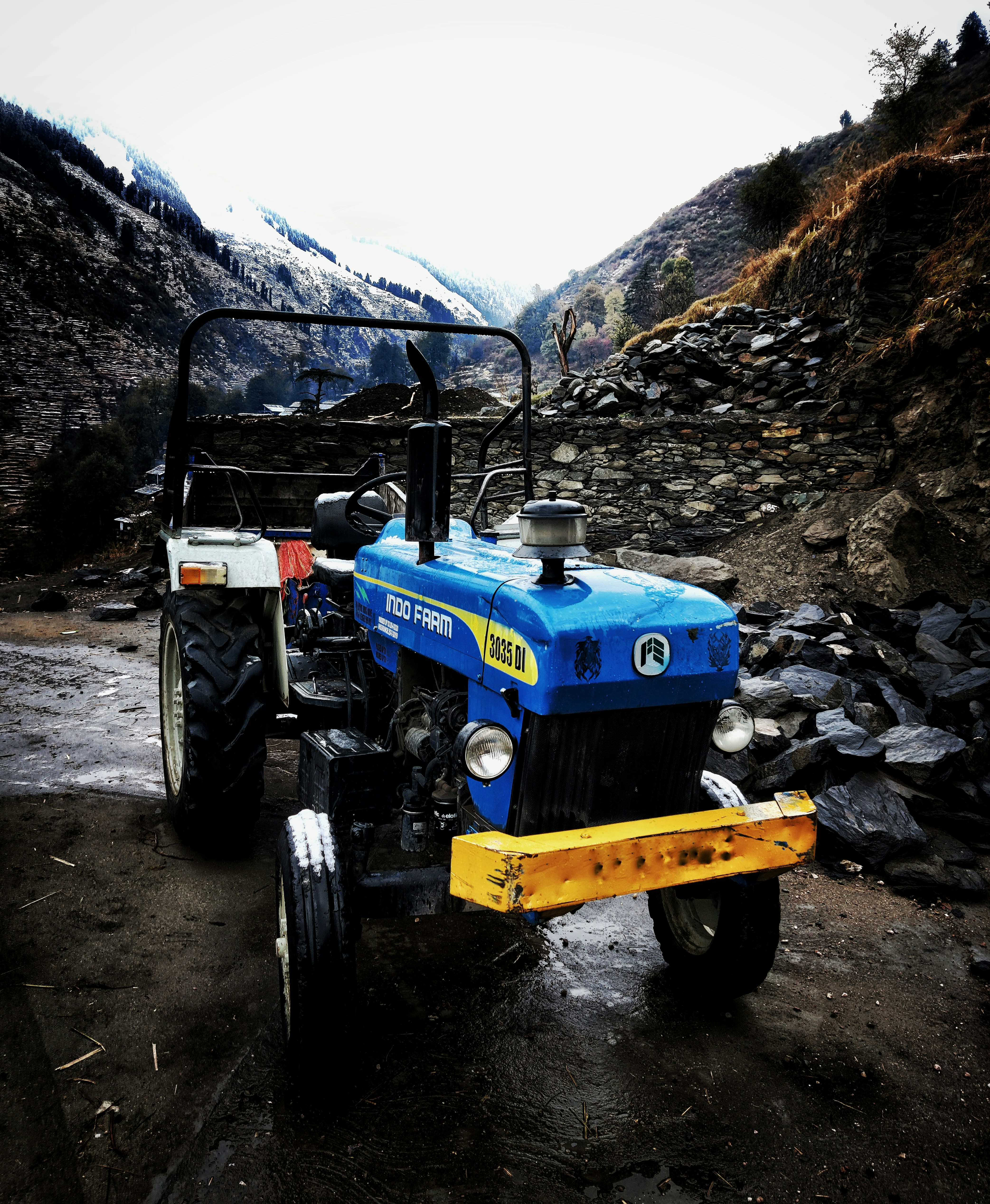 Blue and yellow tractor on rocky ground near mountain during daytime ...