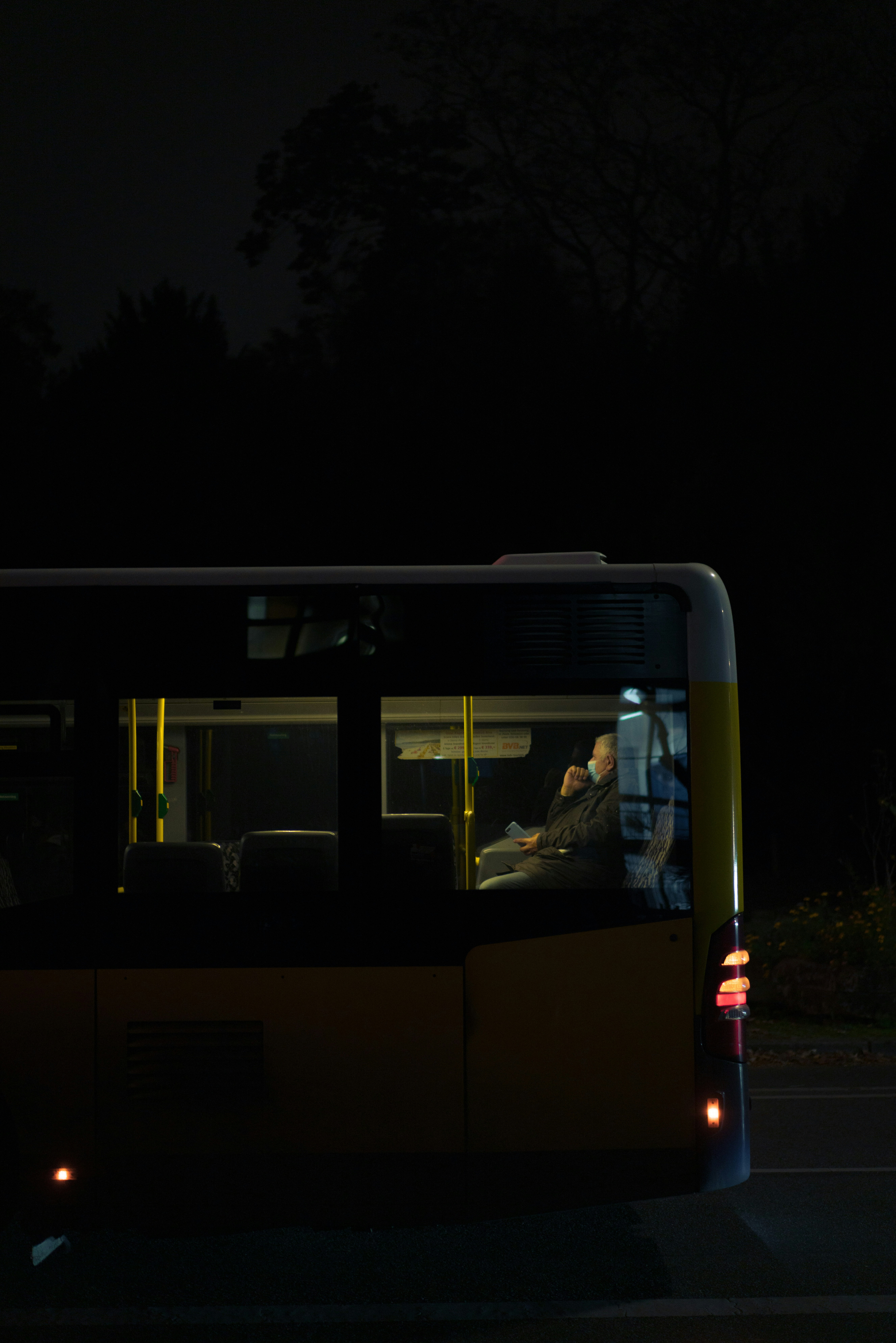 A solitary figure seated on a bus, illuminated by soft interior lights against the dark backdrop of night. The scene evokes a sense of quiet reflection.