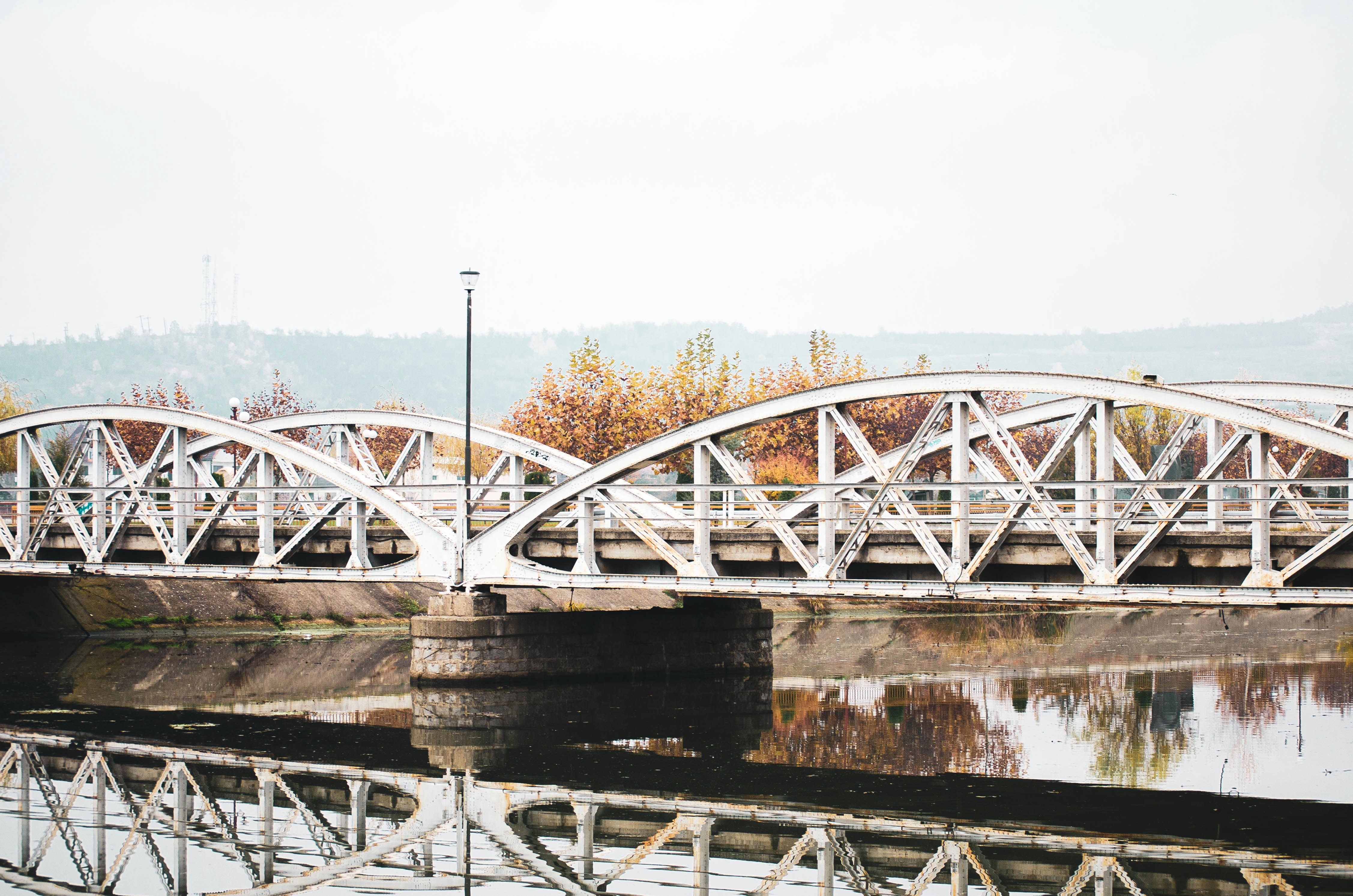 White arched bridge spans a calm river, reflecting seasonal foliage.