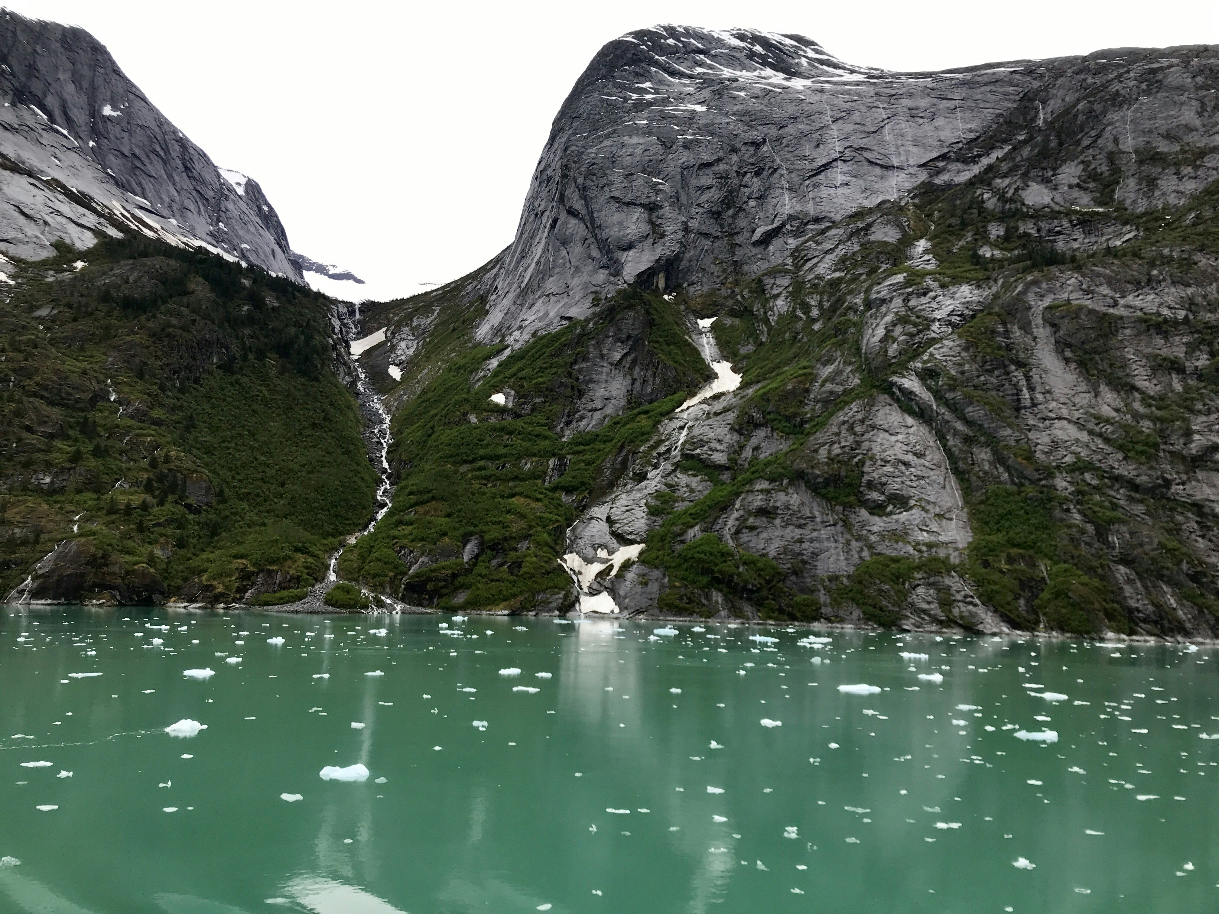 Steep cliffs rise above turquoise waters dotted with ice in Alaska's Tracy Arm Fjord.