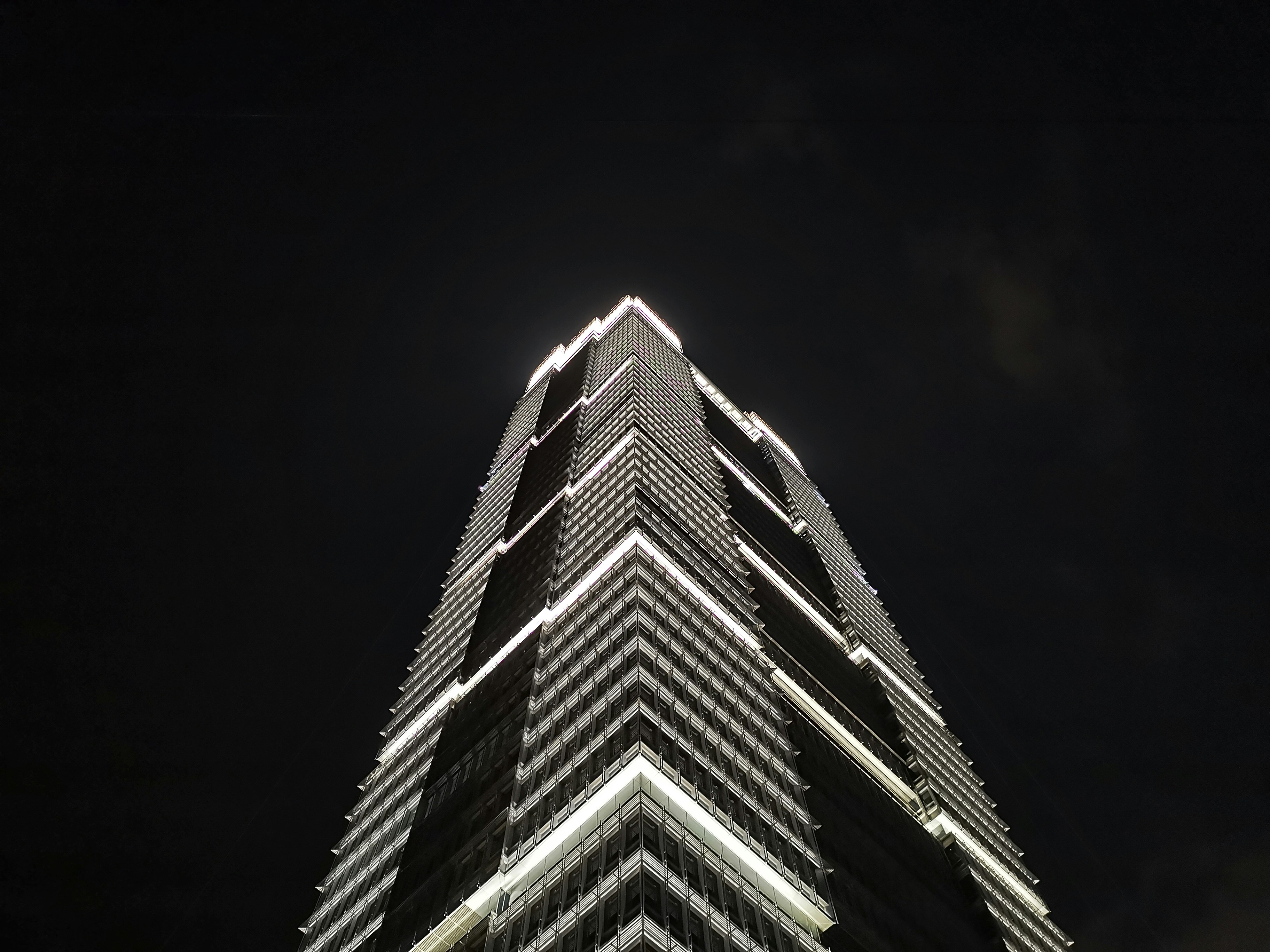 Illuminated skyscraper reaching towards the night sky, showcasing sleek architectural lines and vibrant lighting.