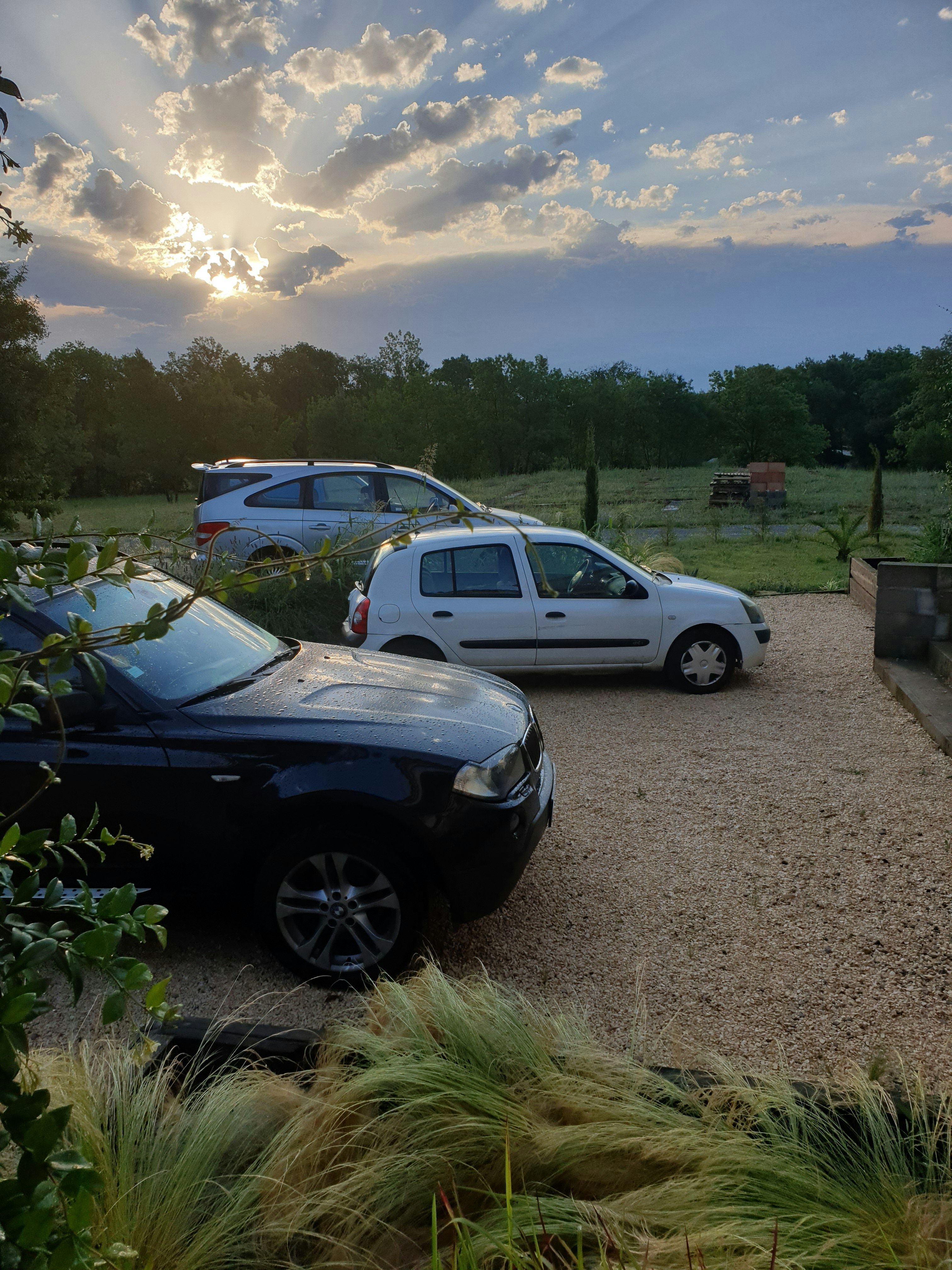 Sunlit Parking Lot: Cars, Gravel, and a Quiet Field at Dusk